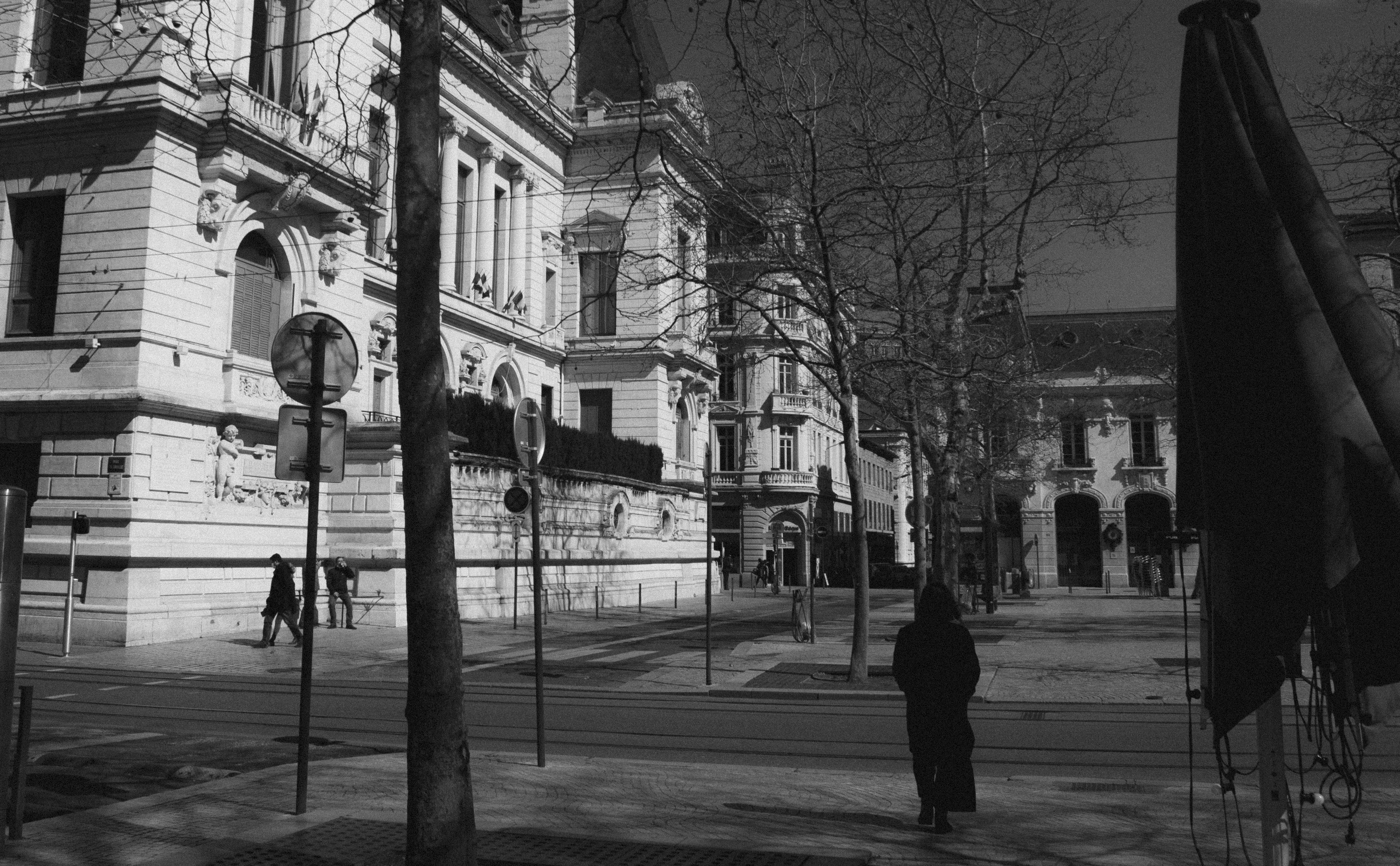 Black and white streetscape with a solitary figure near historic buildings and bare trees.