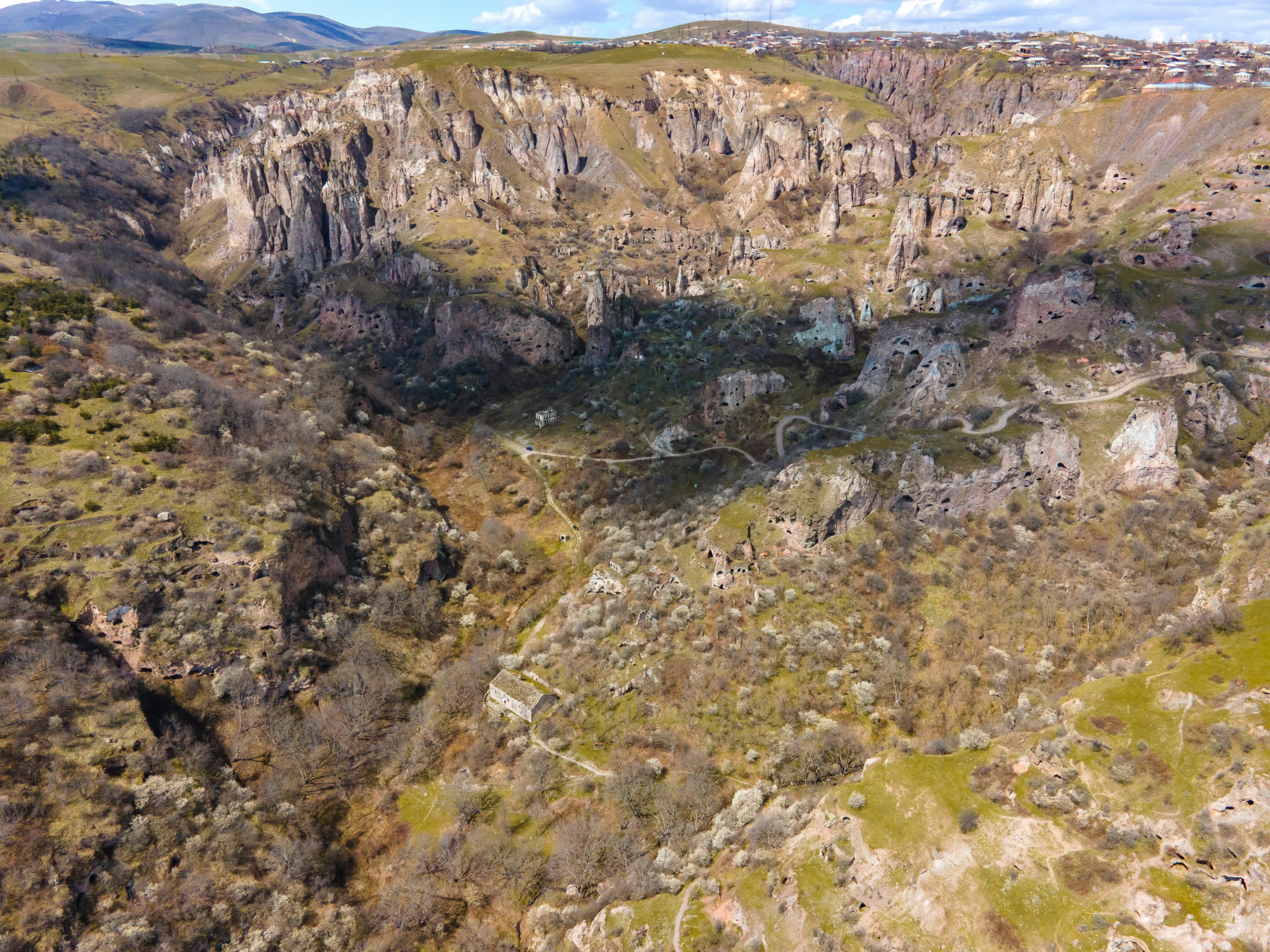 Expansive view of a rugged canyon with steep cliffs and lush greenery, showcasing the interplay of natural textures and geological formations.