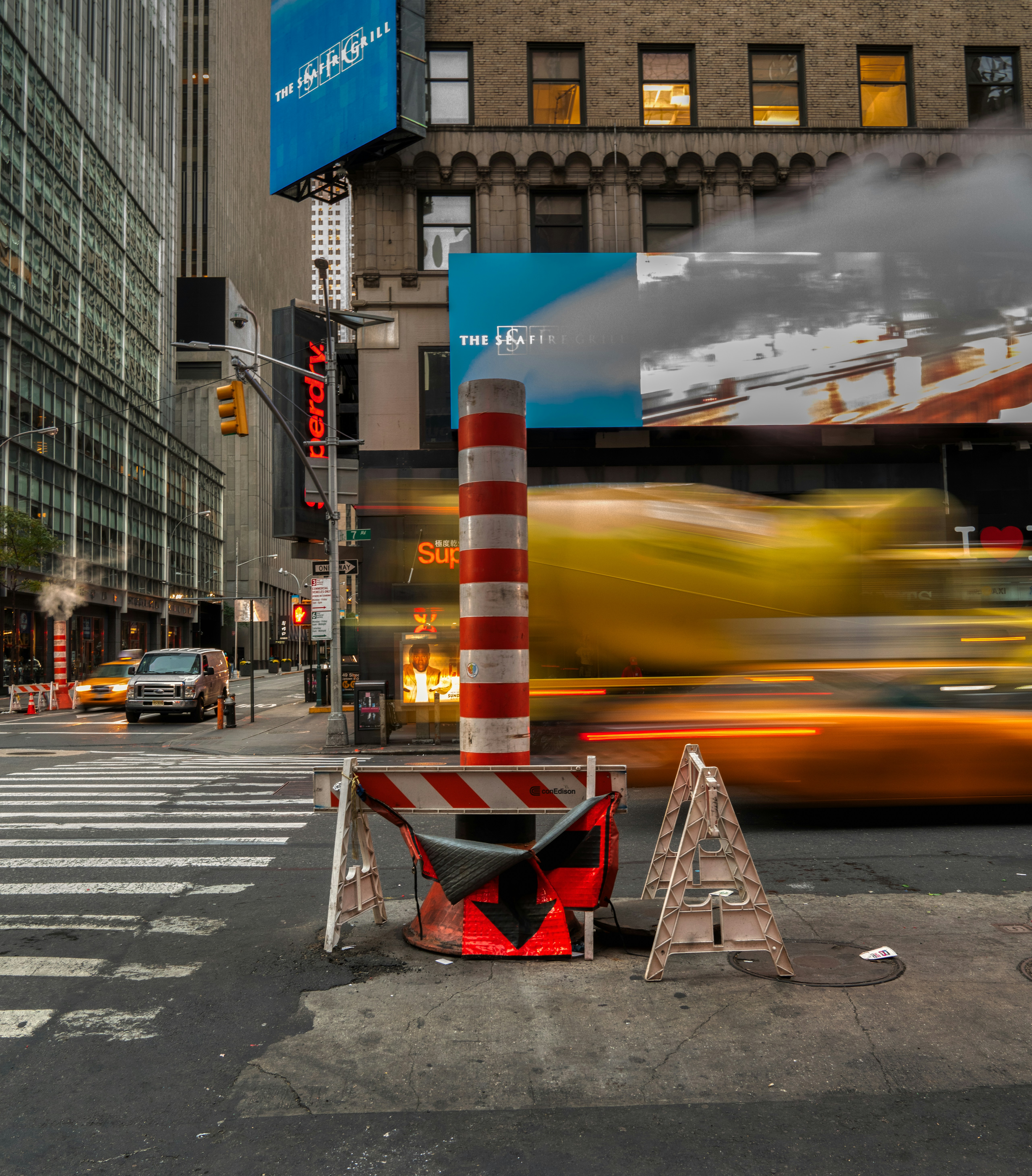 A bustling city intersection with a blurred yellow taxi speeding past a construction barrier, capturing the essence of urban energy. The surrounding buildings reflect the dynamic atmosphere of city life.