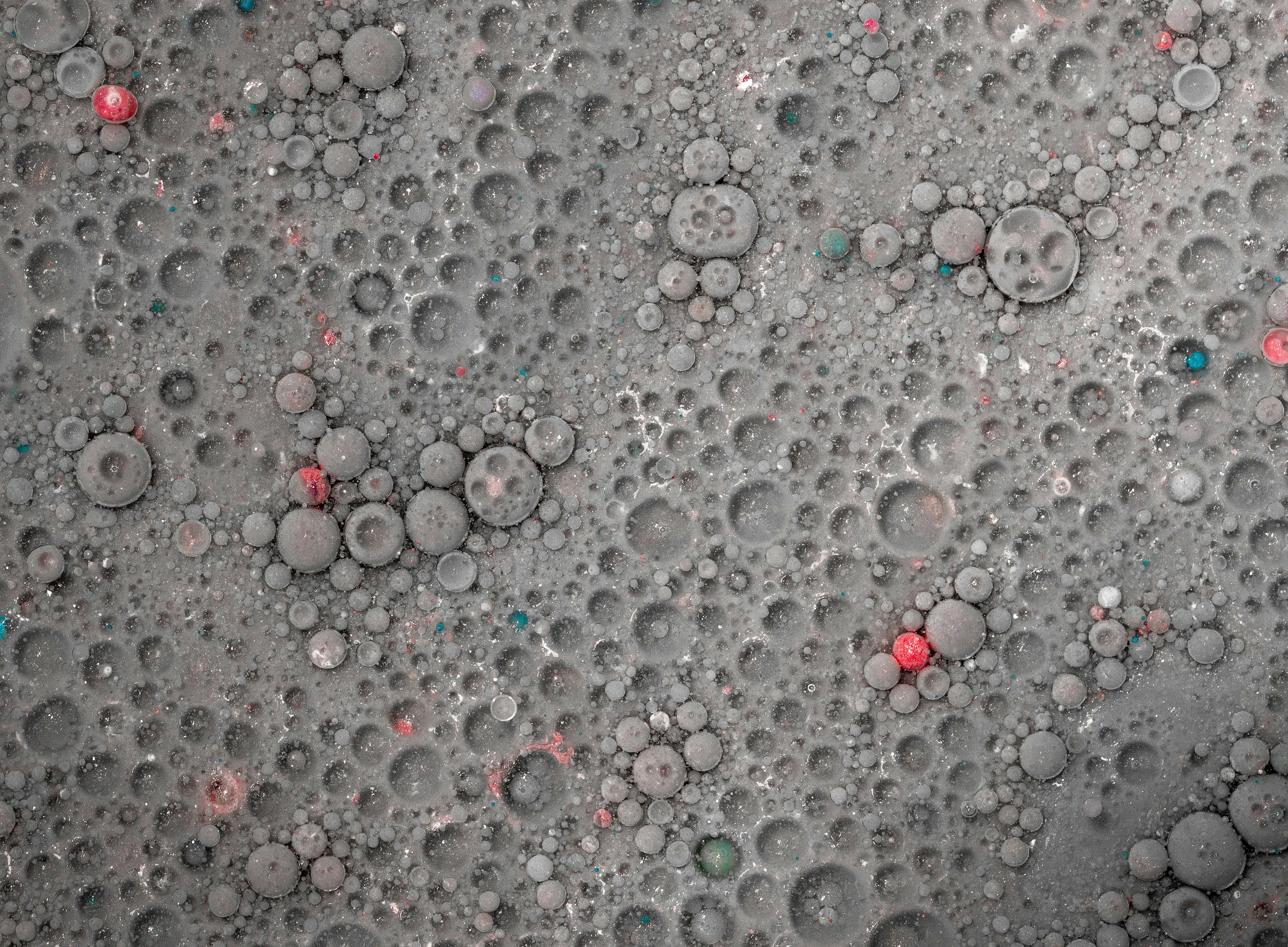 Abstract pattern of various-sized bubbles with occasional red accents on a grey background.