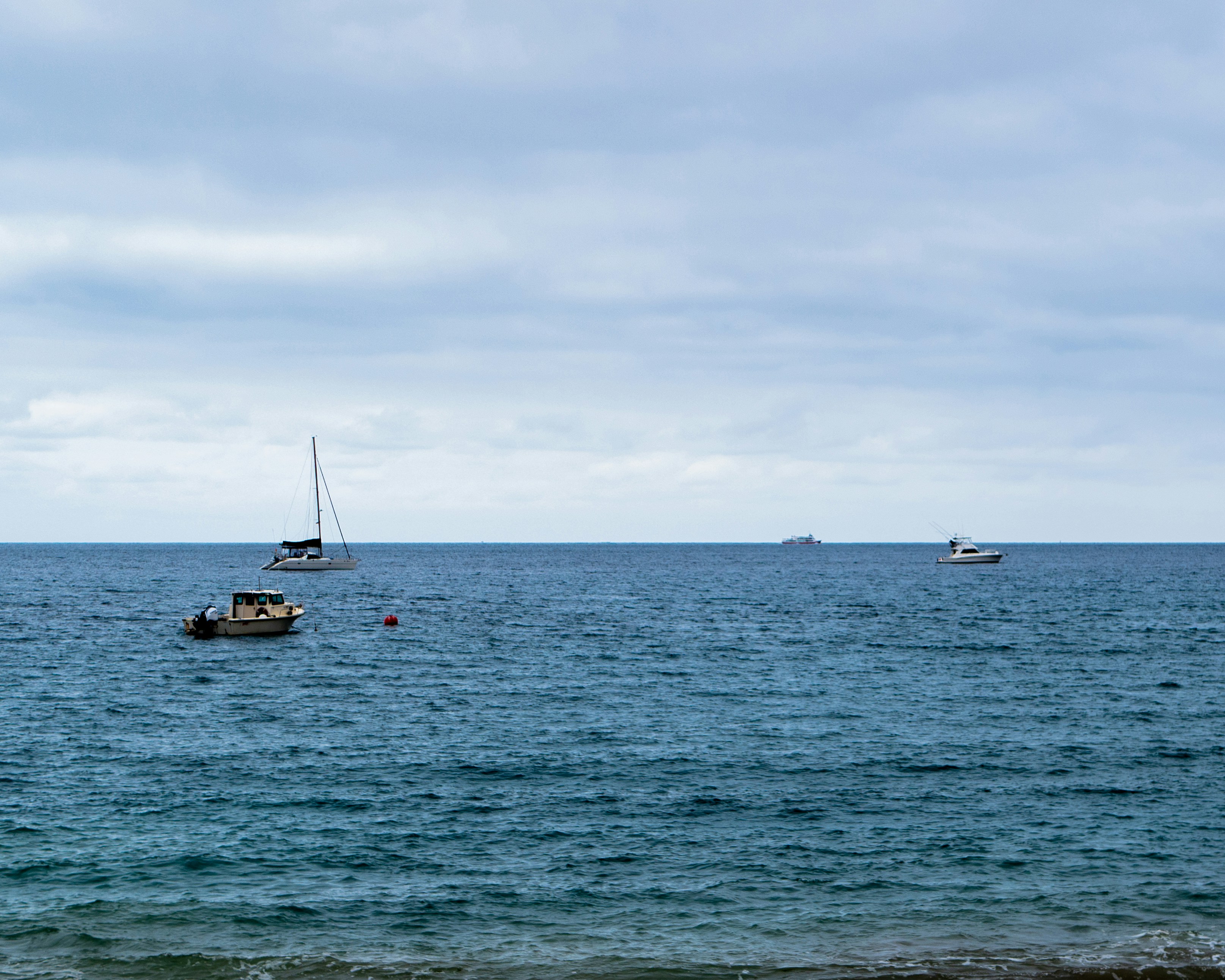 Sailboats and motorboats gently bob on a tranquil sea under a cloudy sky, showcasing the peaceful coexistence of nature and human activity.