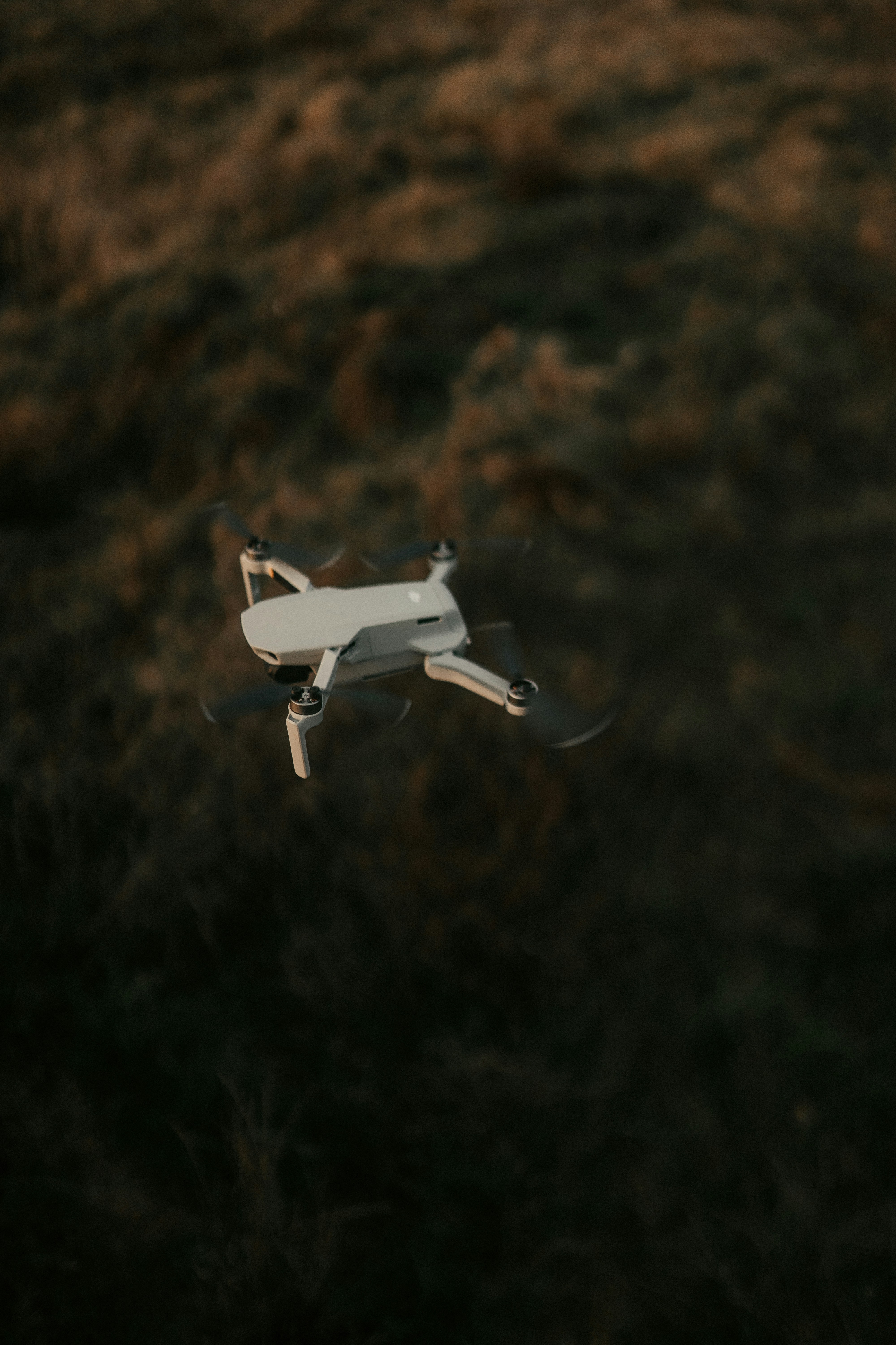 A white drone hovers mid-air against a blurred background of earthy tones, showcasing its sleek design and technology.