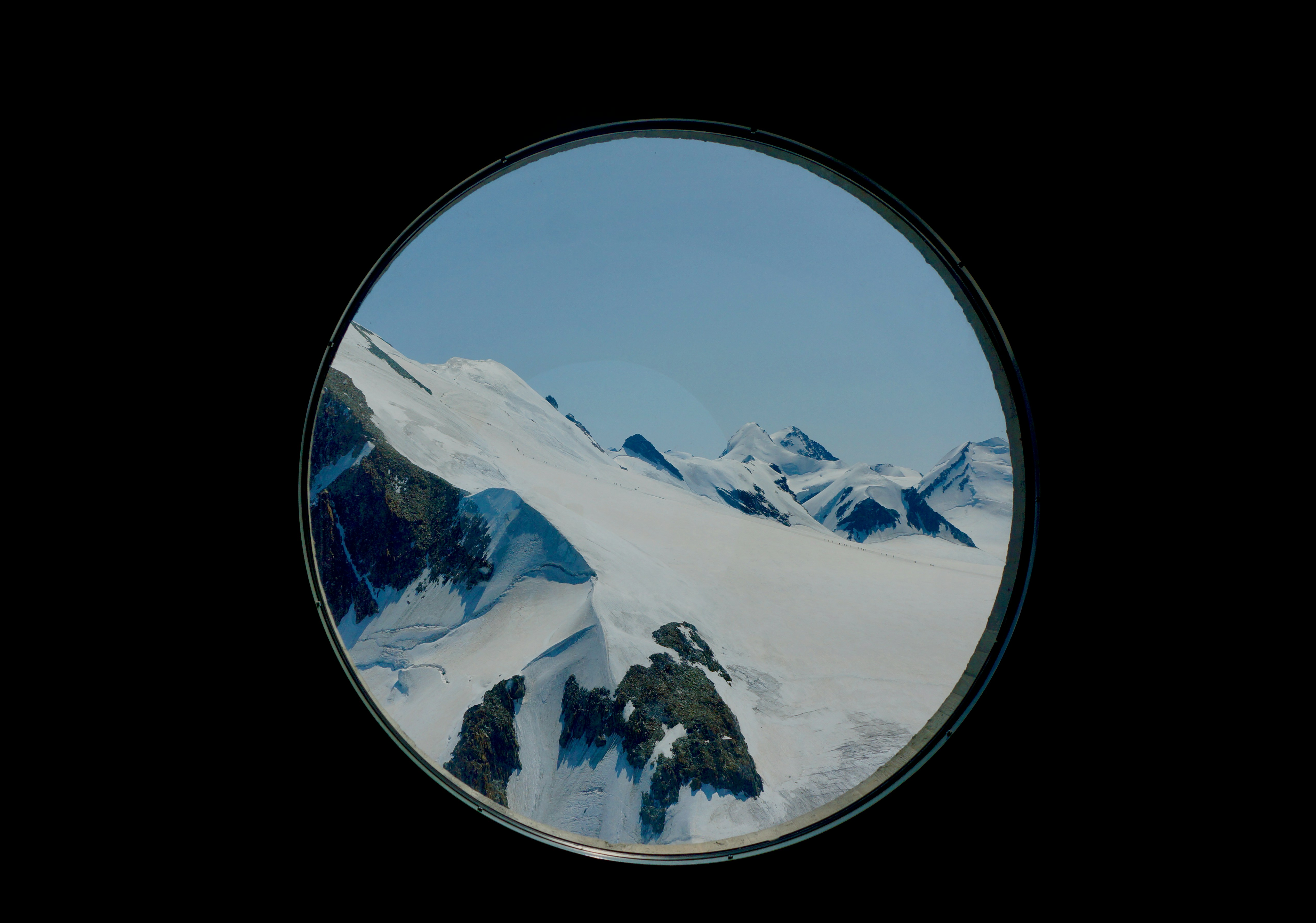 Snow-capped mountains and expansive glaciers viewed through a circular window, highlighting the stark beauty of a remote landscape.