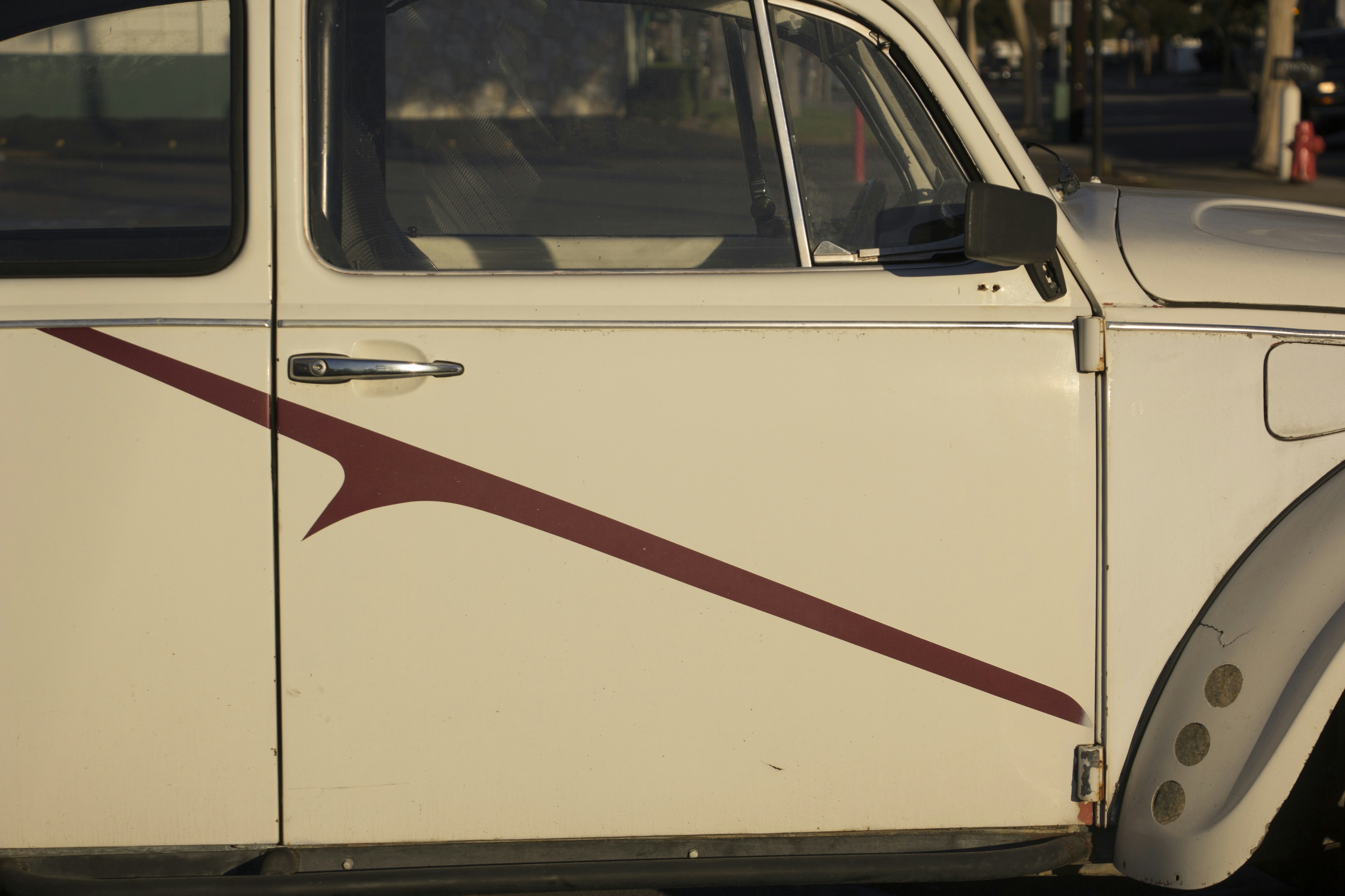 Close-up of a vintage Volkswagen Beetle showcasing its iconic design features and a distinctive maroon stripe along the side.