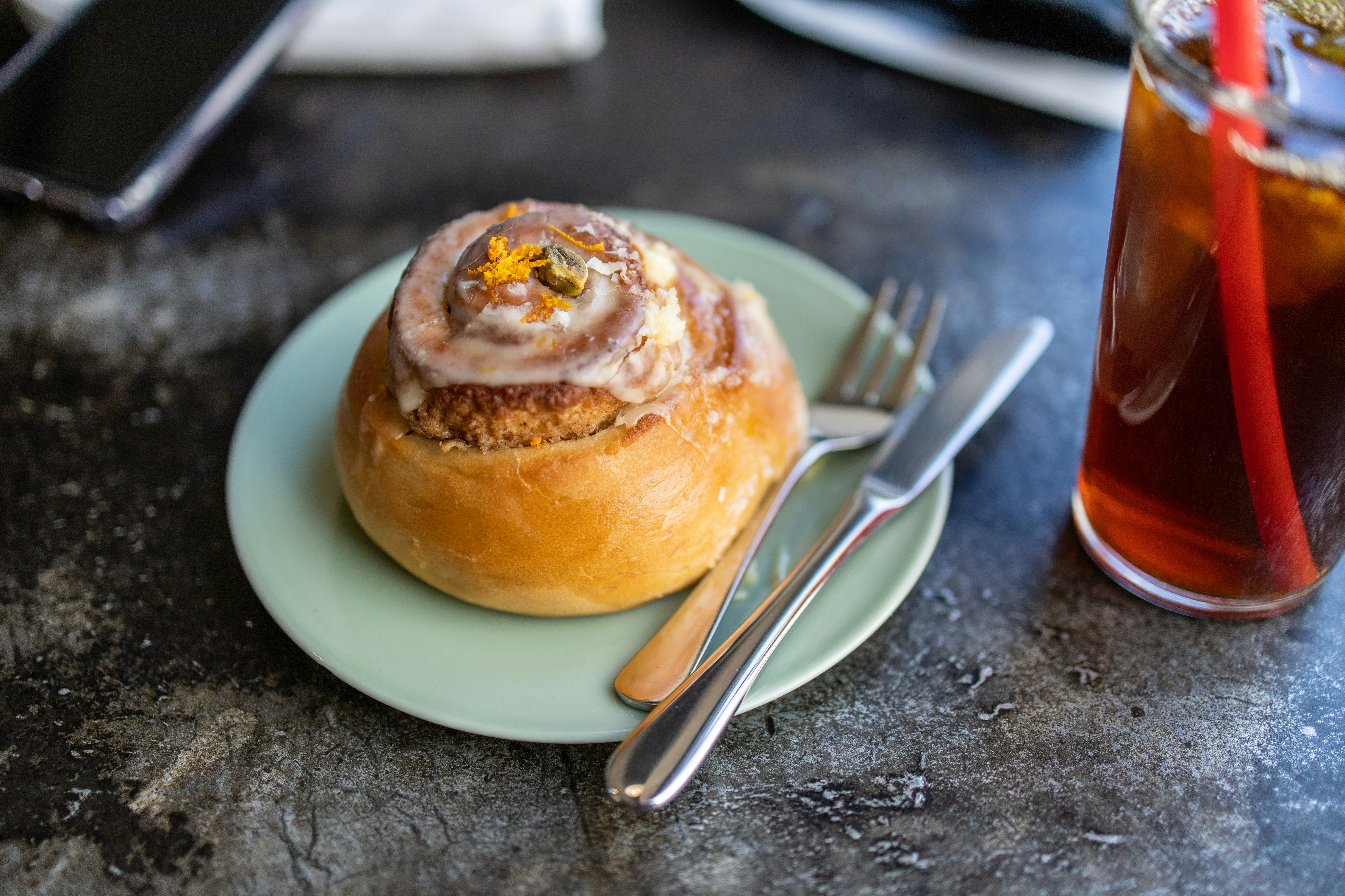 Cinnamon Roll on a Mint Plate with Iced Tea at Table Edge