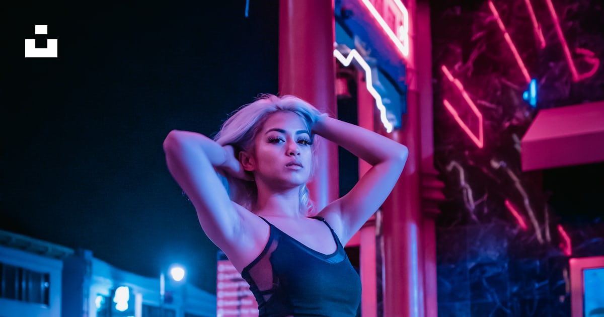 검은 스포츠 브래지어와 파란색 데님 청바지를 입은 여자가 빨간 네온 불빛 간판 옆에 서 있습니다 사진 Unsplash의 무료