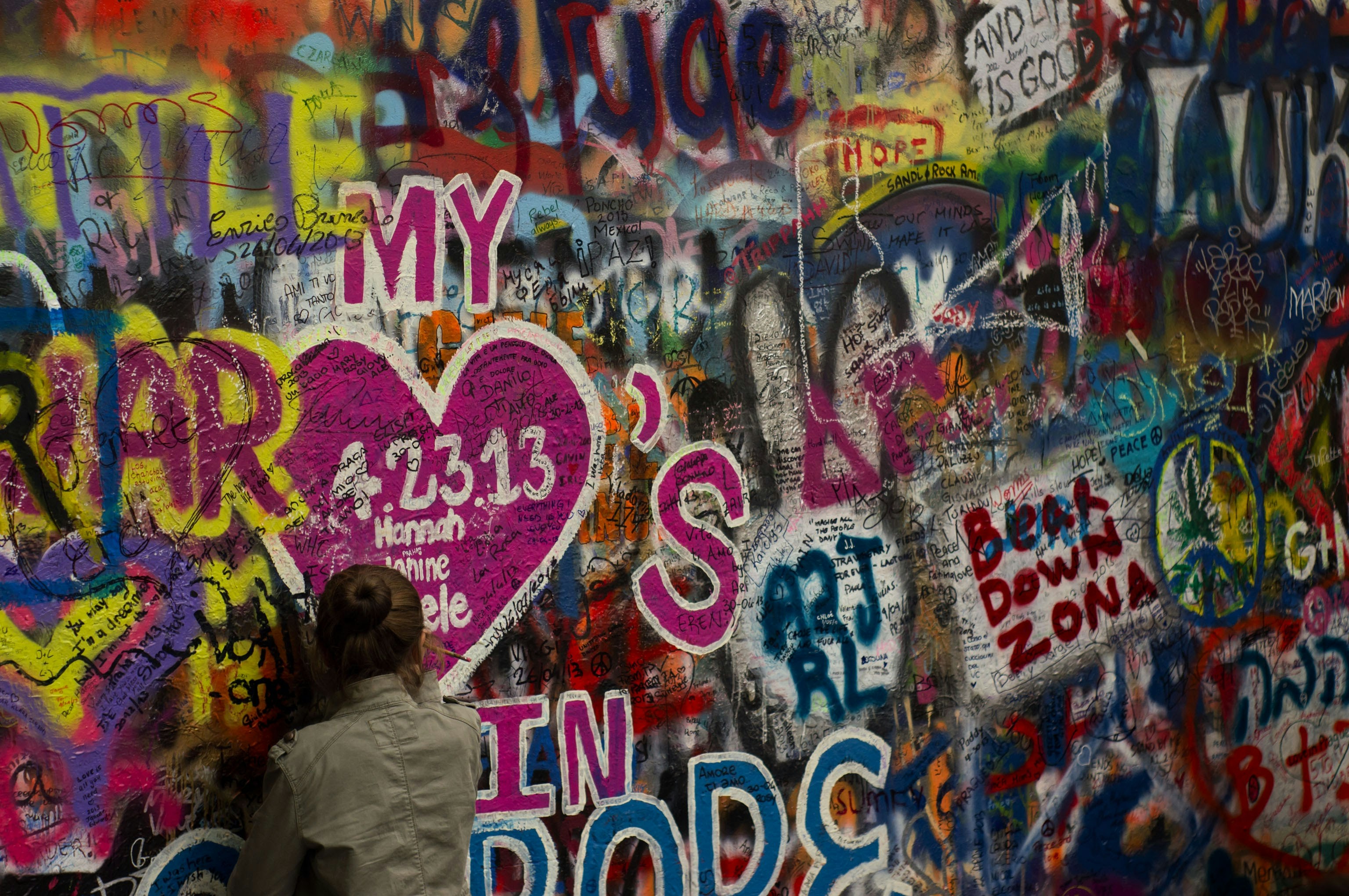 Person adding to a colorful graffiti wall covered in messages and designs.
