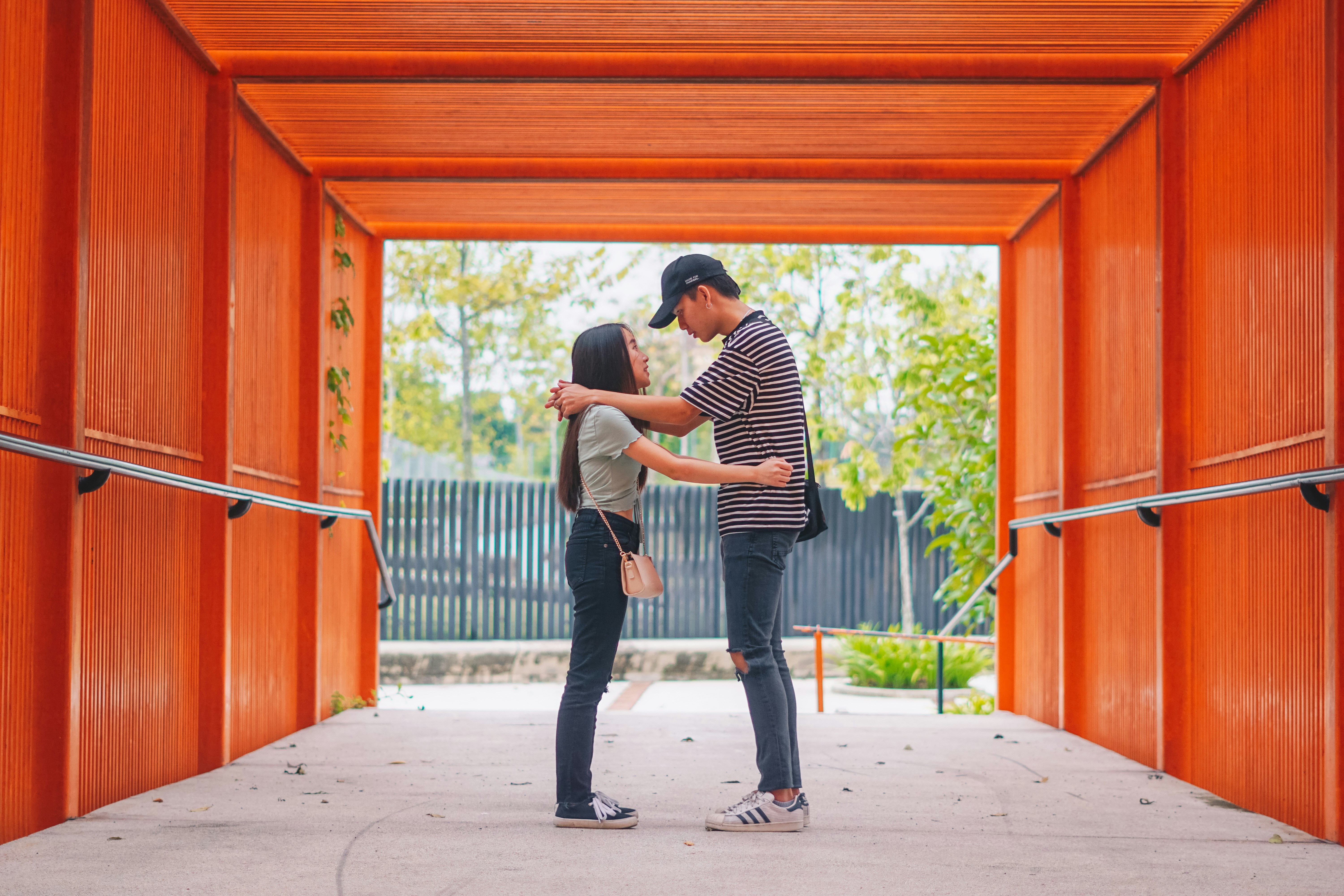 Couple sharing a tender moment in a vibrant orange corridor surrounded by greenery.
