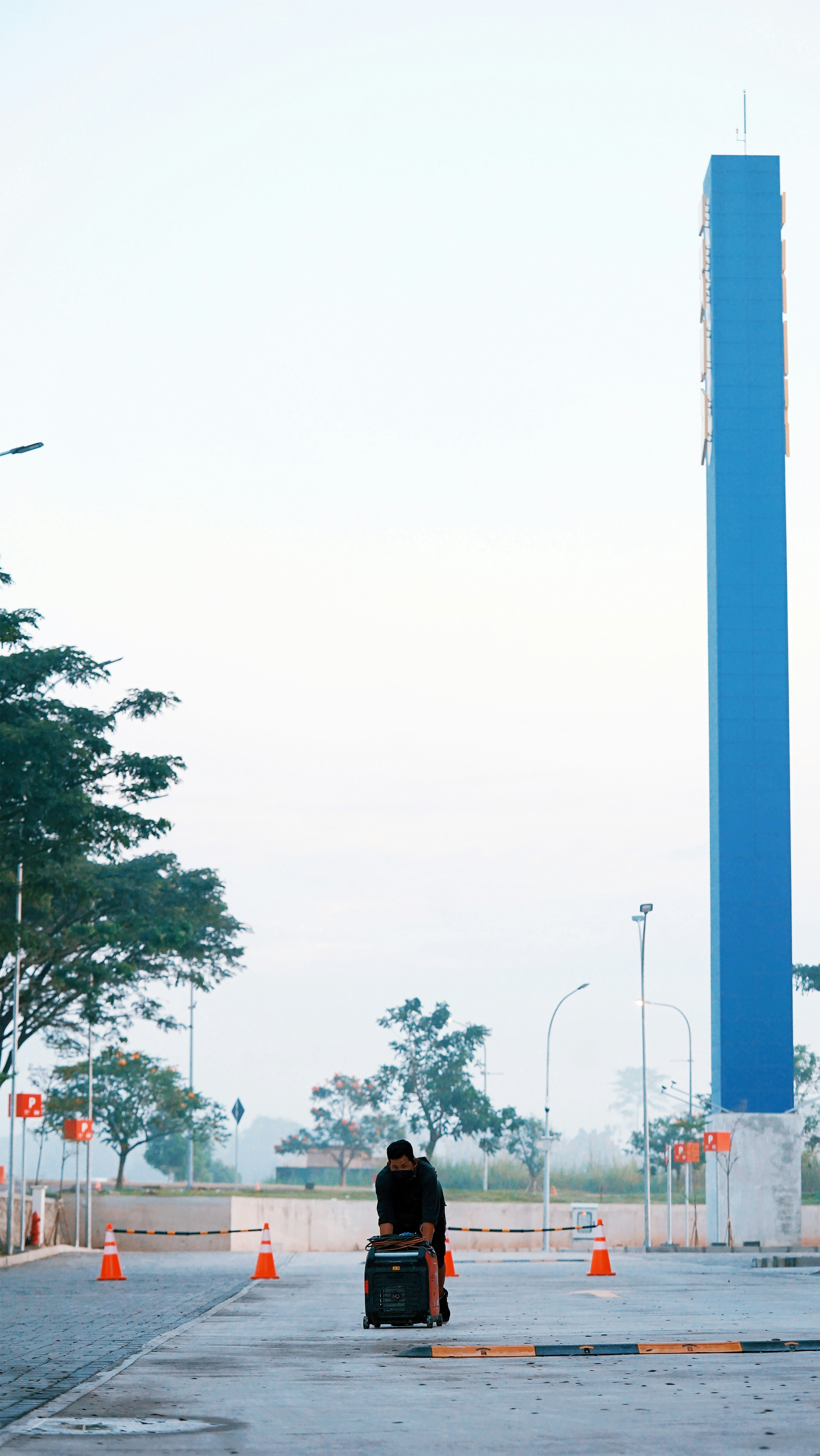 Urban Solitude Beneath the Cyan Tower: A Traveler with a Rolling Luggage