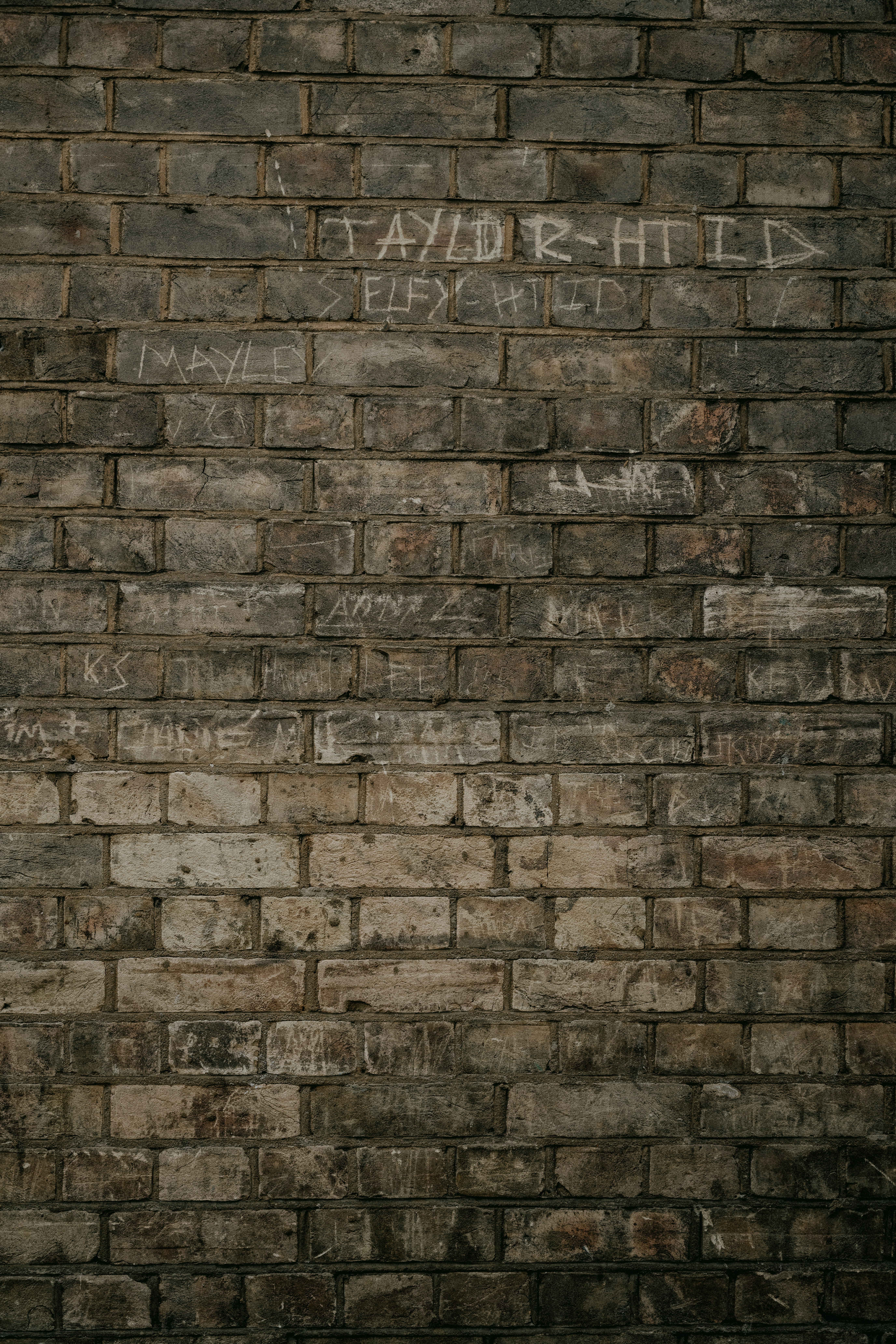 Weathered brick wall adorned with faint chalk inscriptions, capturing the essence of forgotten messages and memories.