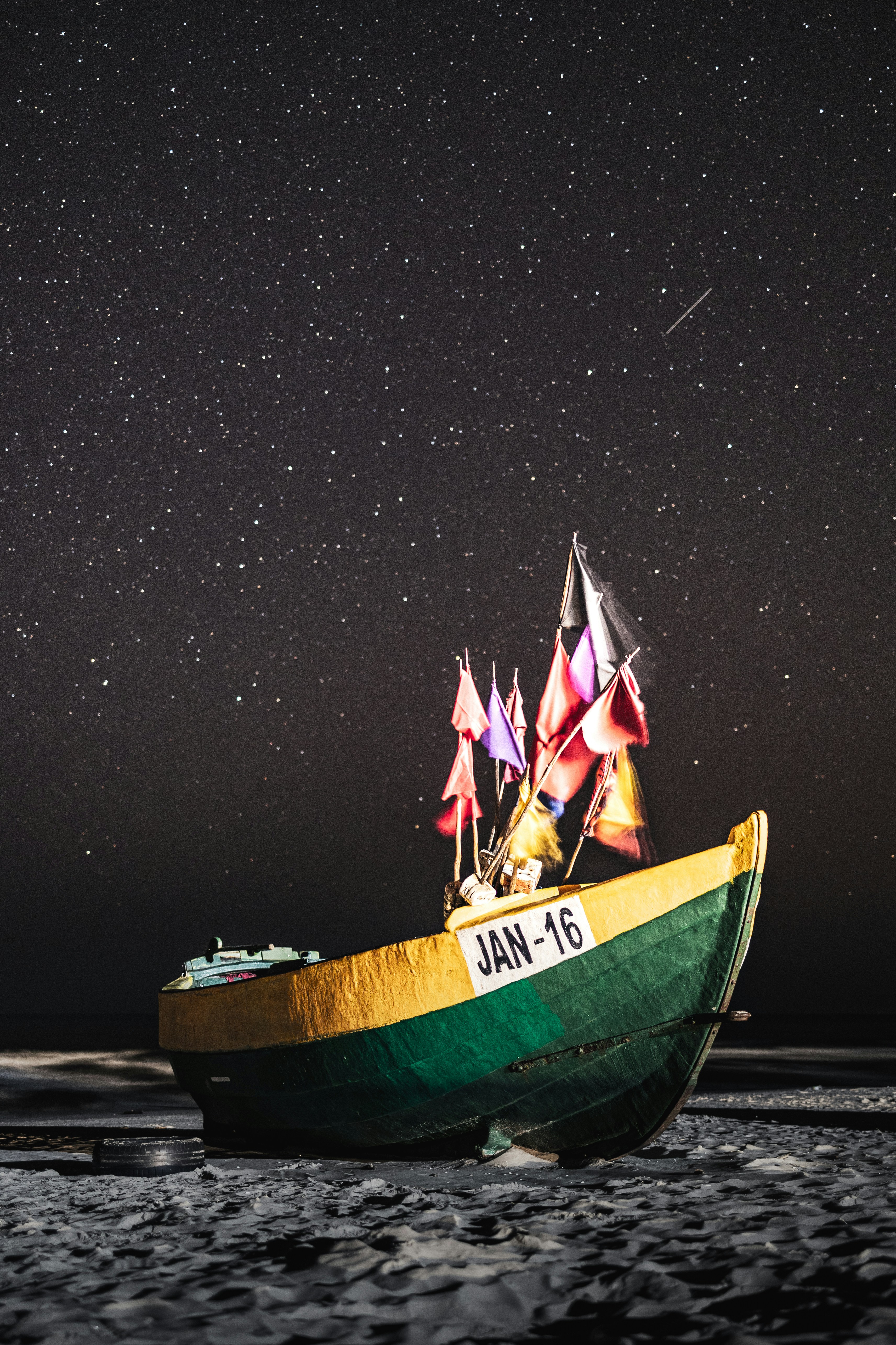 A vibrant fishing boat adorned with colorful flags rests on a sandy beach beneath a star-filled sky.