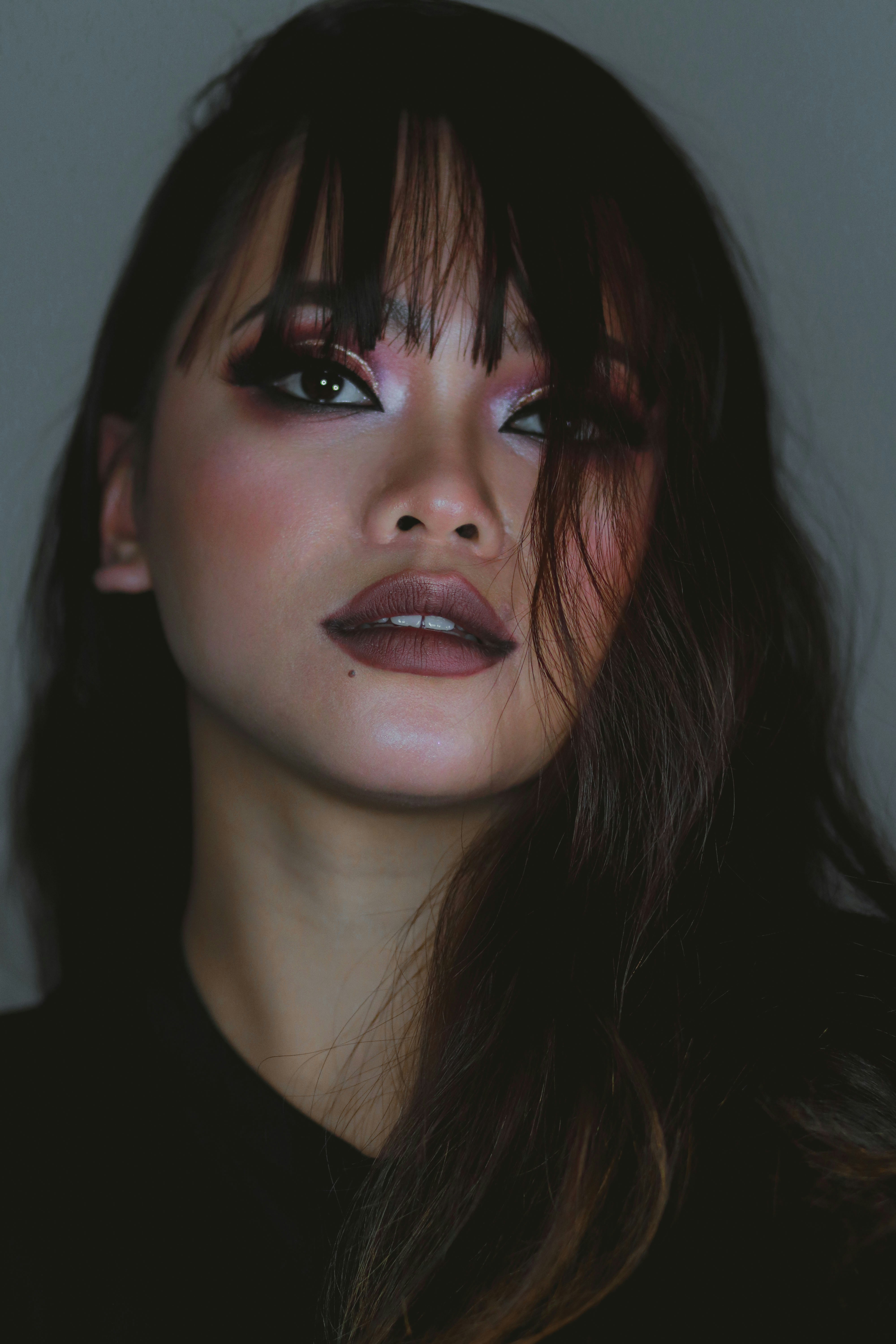 Close-up portrait highlighting striking makeup and expressive features against a muted background.