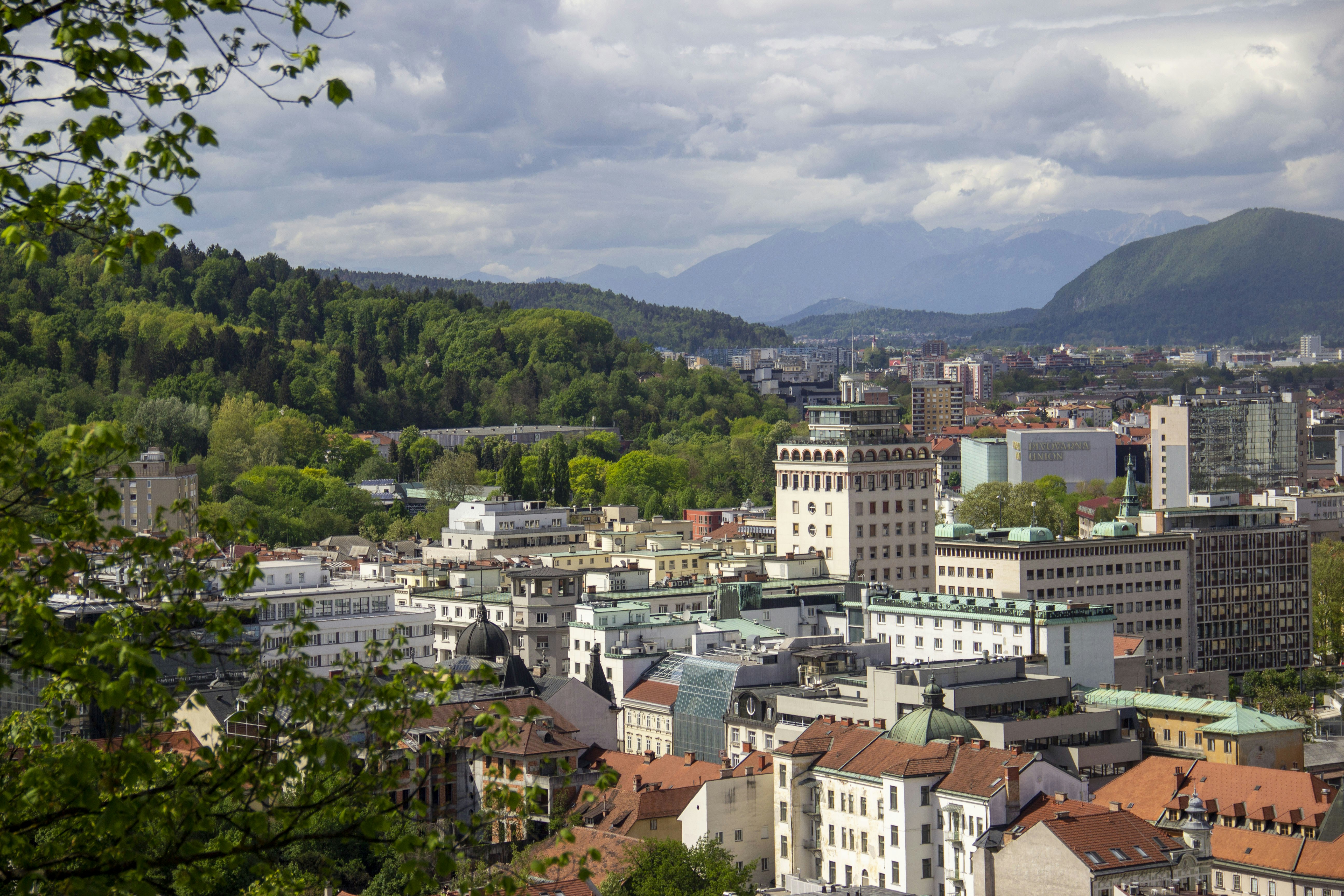A panoramic view of Ljubljana showcasing a blend of modern architecture and lush greenery, with distant mountains framing the skyline.