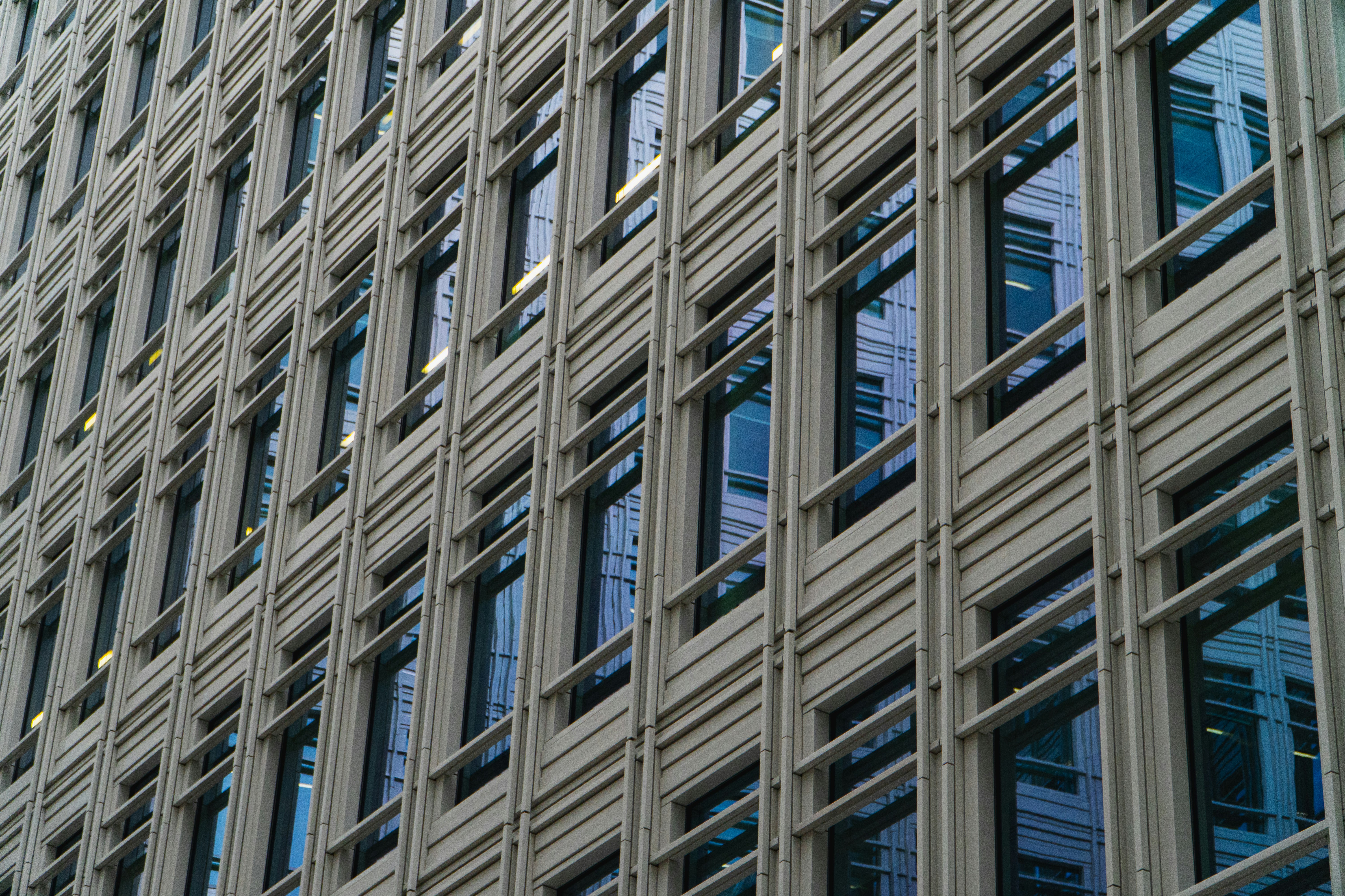 Modern architectural facade showcasing a grid of reflective windows and intricate lines. The interplay of light and shadow enhances the design's geometric beauty.