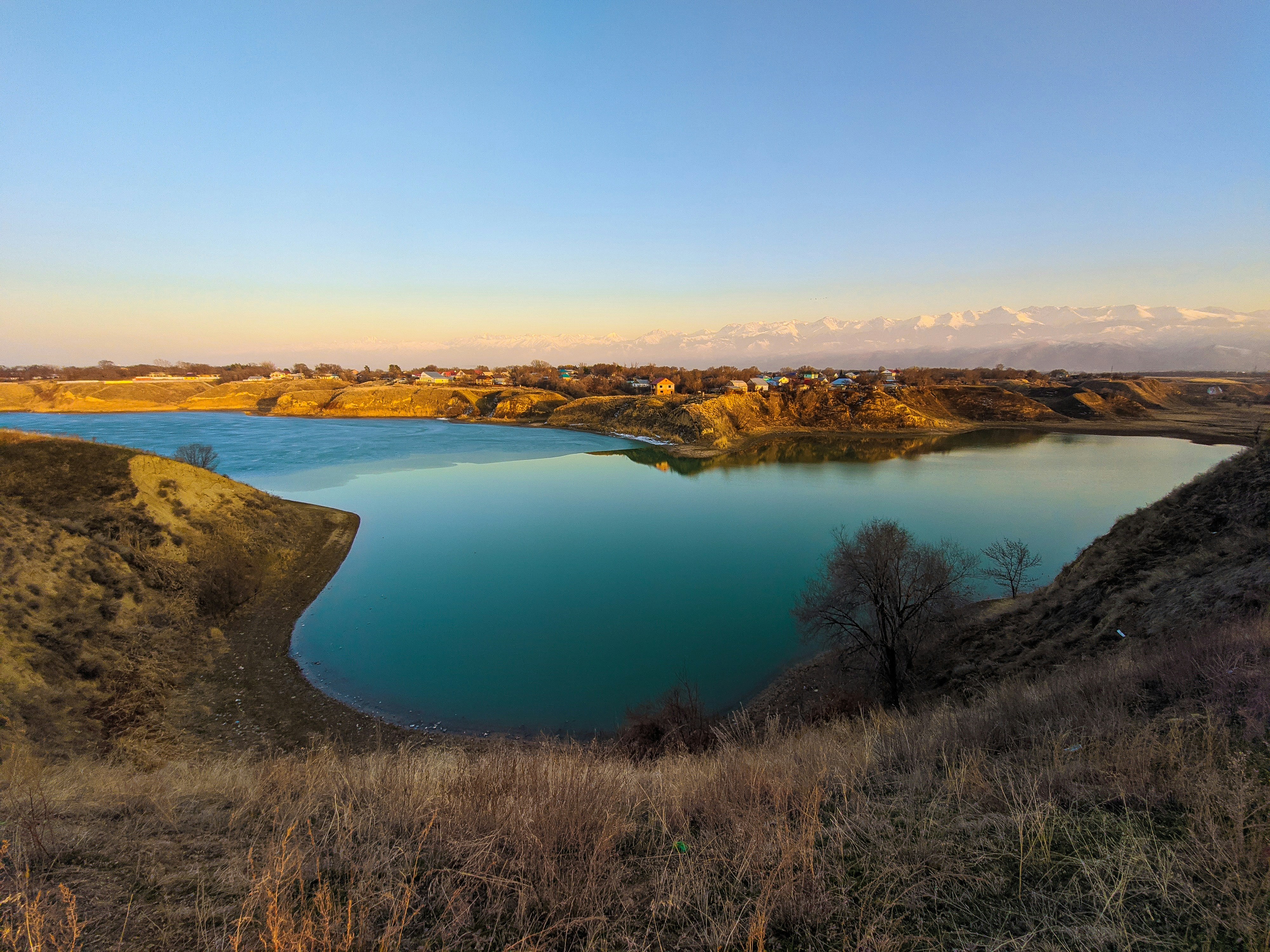 Valley lake winds through golden hills beneath a pastel sky, with dry foreground grasses in frame.