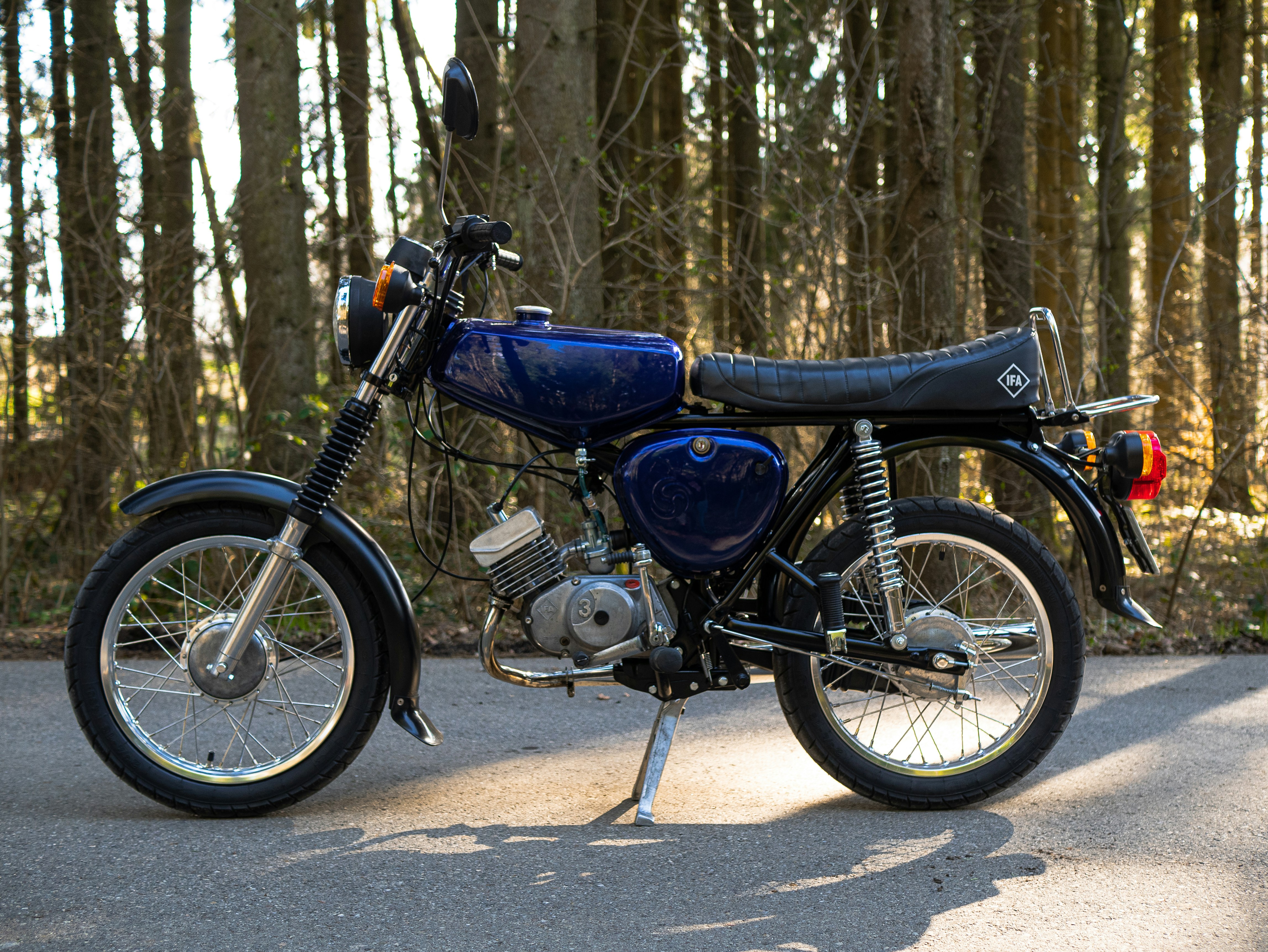 Blue Velvet Chrome: A Classic Motorcycle Resting Under Dappled Forest Light