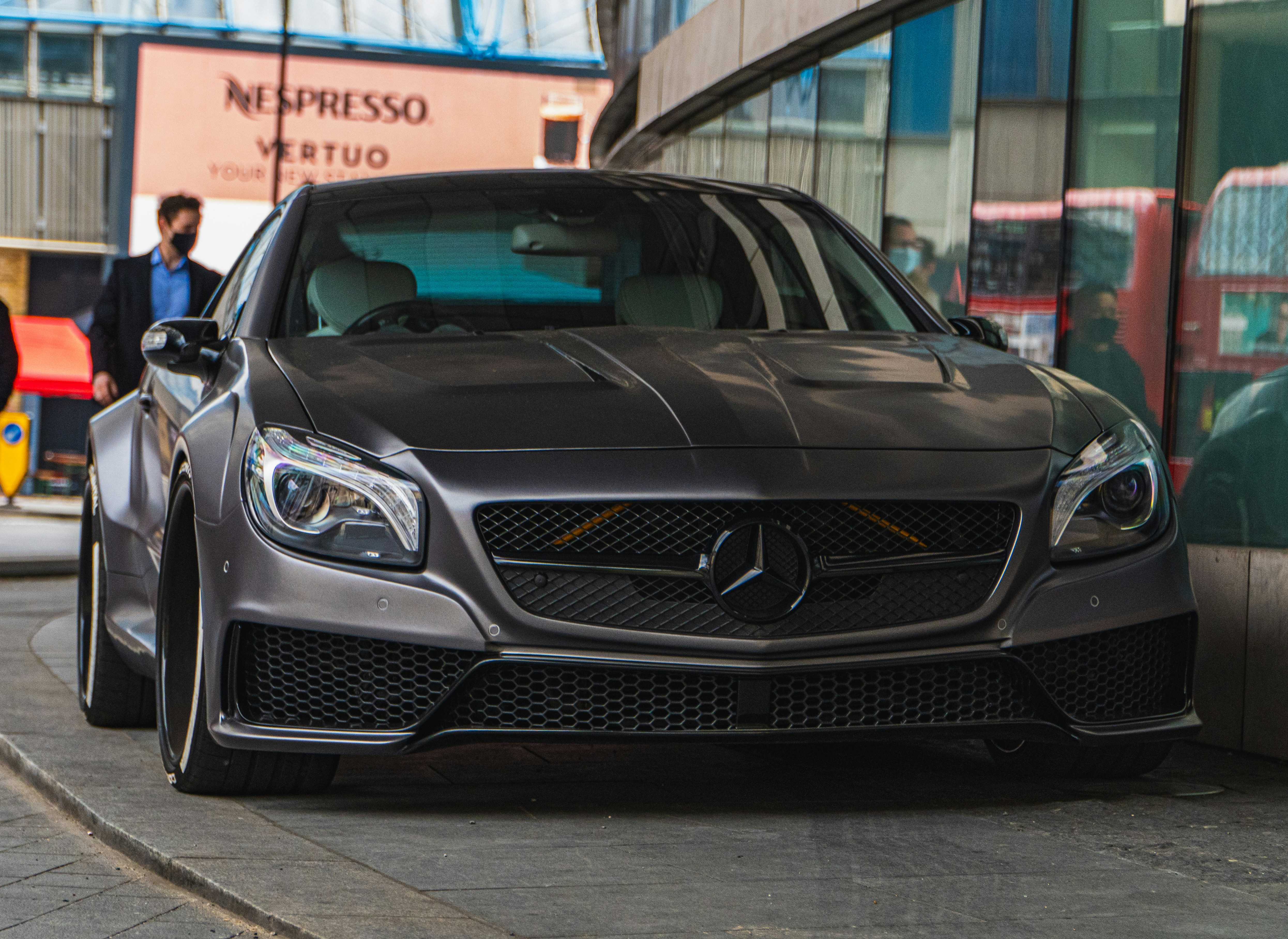 Matte gray Mercedes-Benz sports car parked against a modern urban backdrop, showcasing its aerodynamic design and distinctive grille.