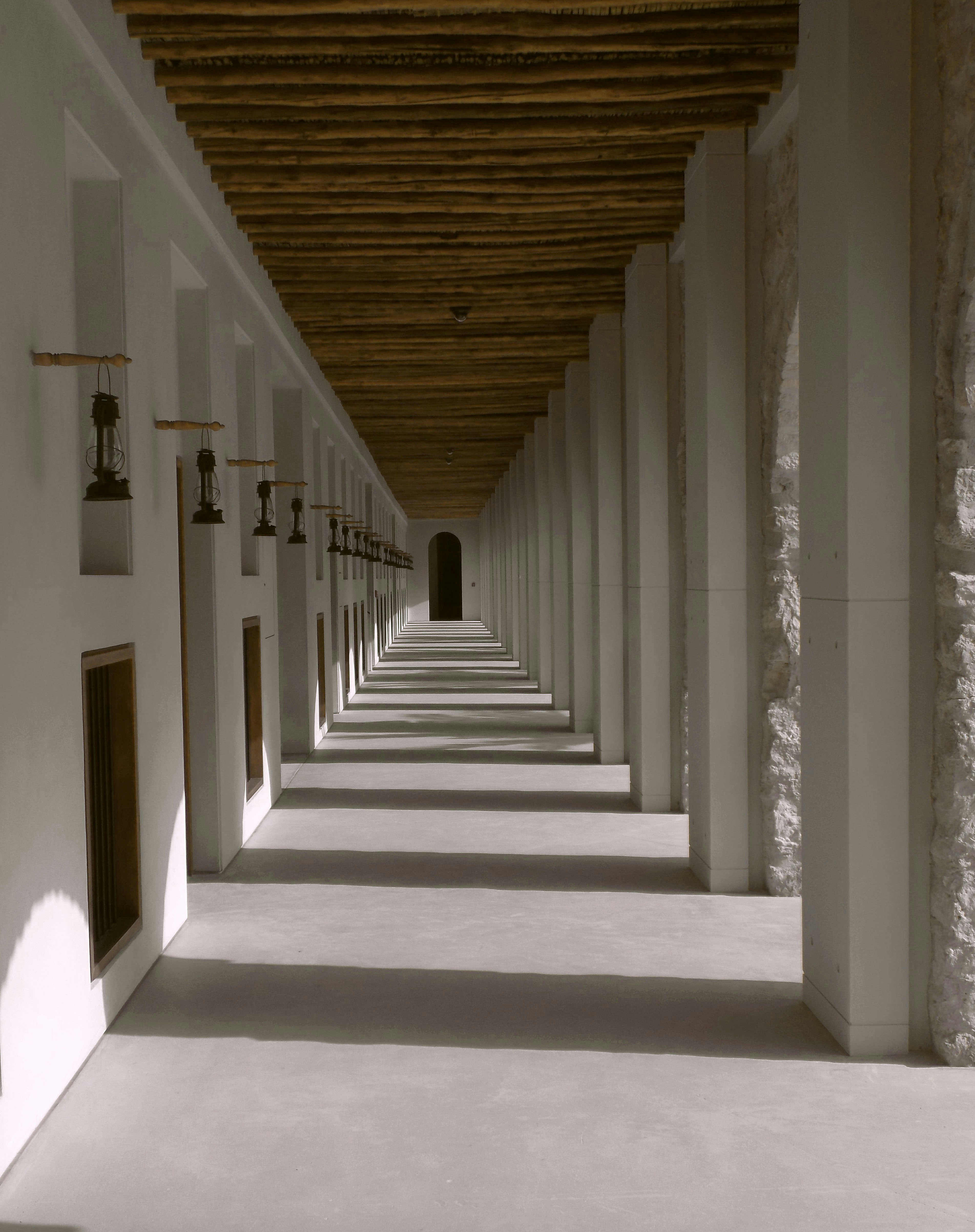 Long corridor with hanging lanterns and textured walls, leading to a dark doorway at the end.