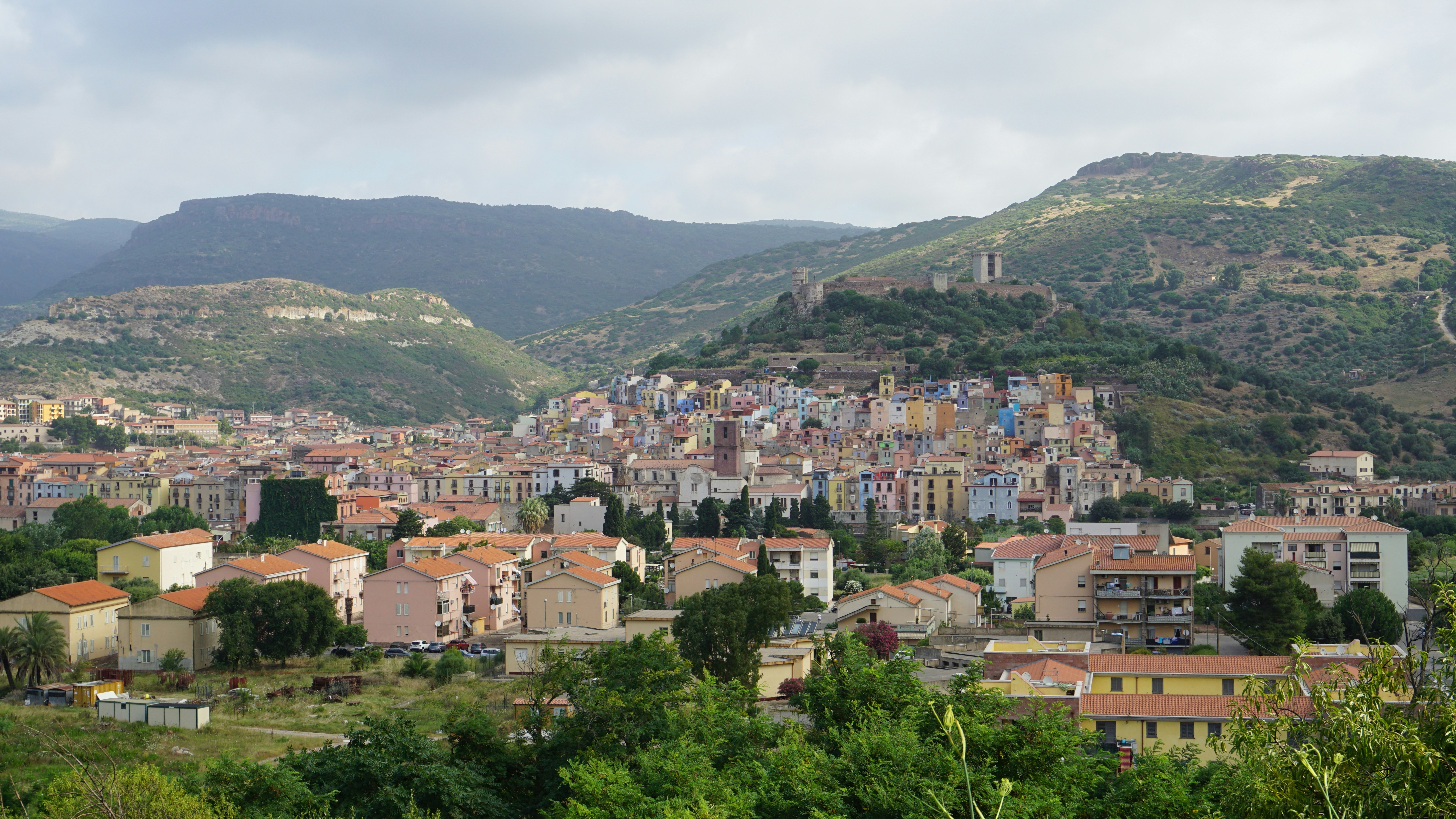Vibrant hillside village showcasing a mosaic of colorful buildings against a mountainous backdrop. Lush greenery frames the scene.