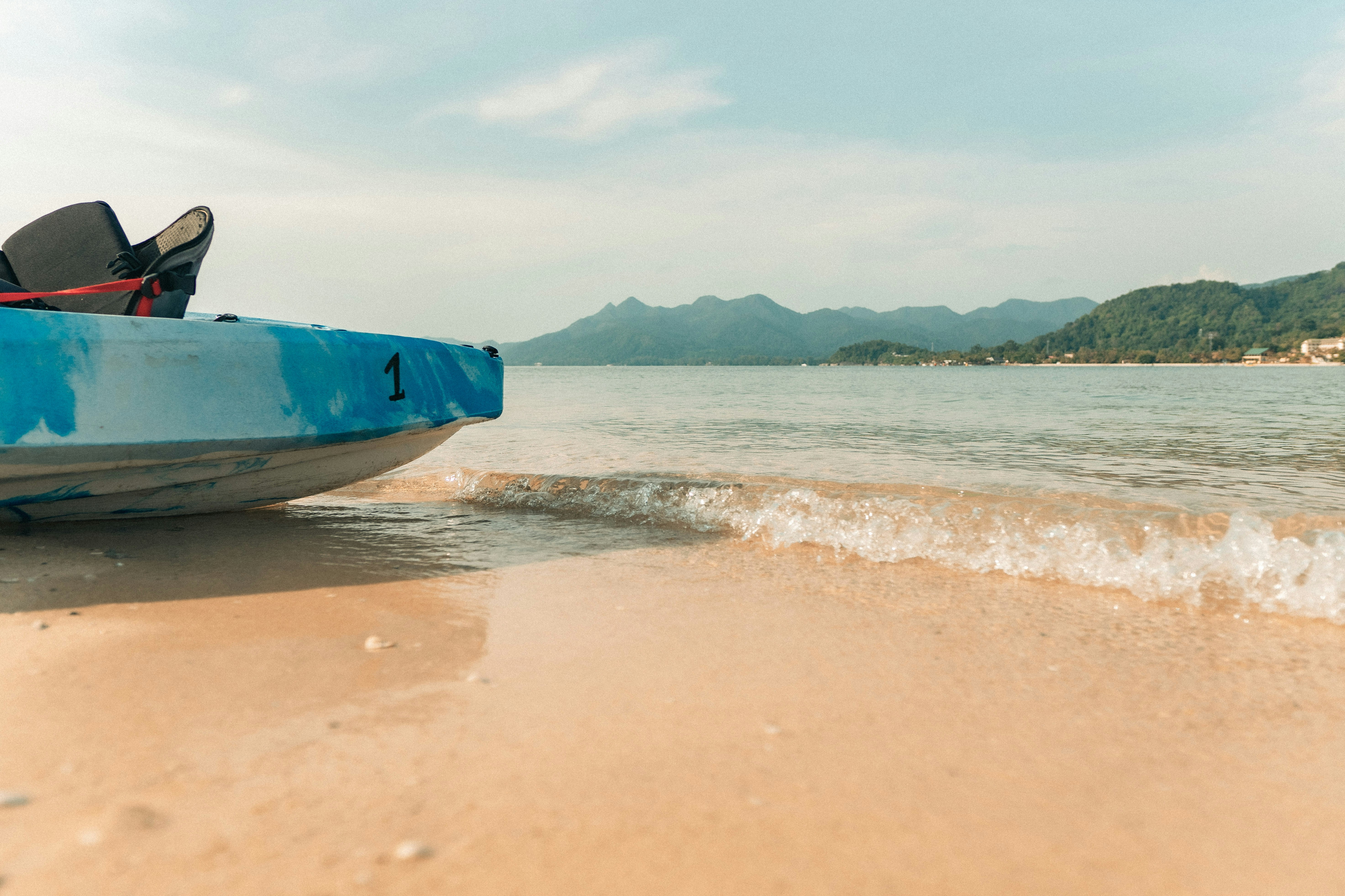 Docked Blue Kayak on Sunlit Beach with Gentle Waves