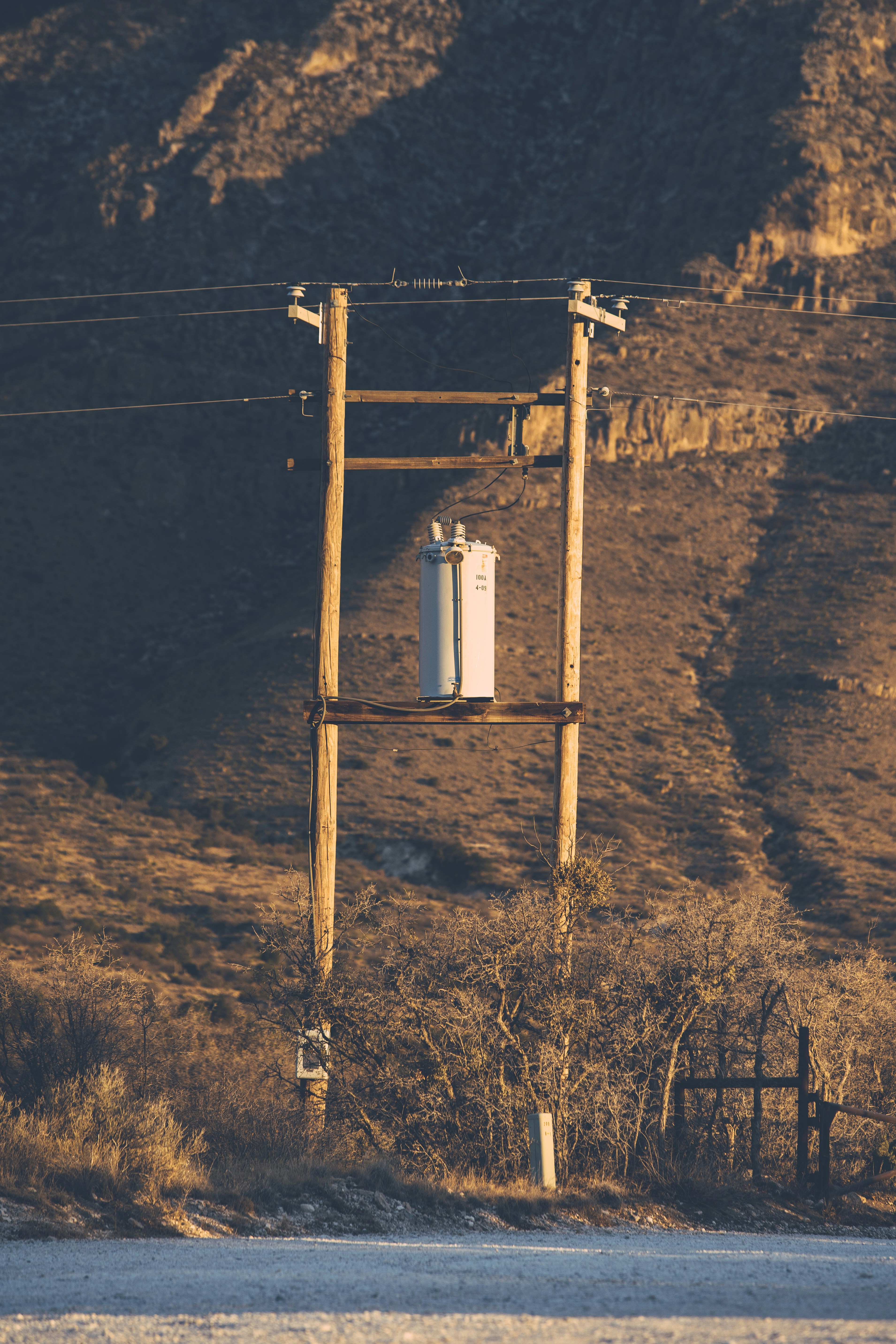Utility pole standing alone in a vast desert landscape, framed by distant mountains and sparse vegetation.