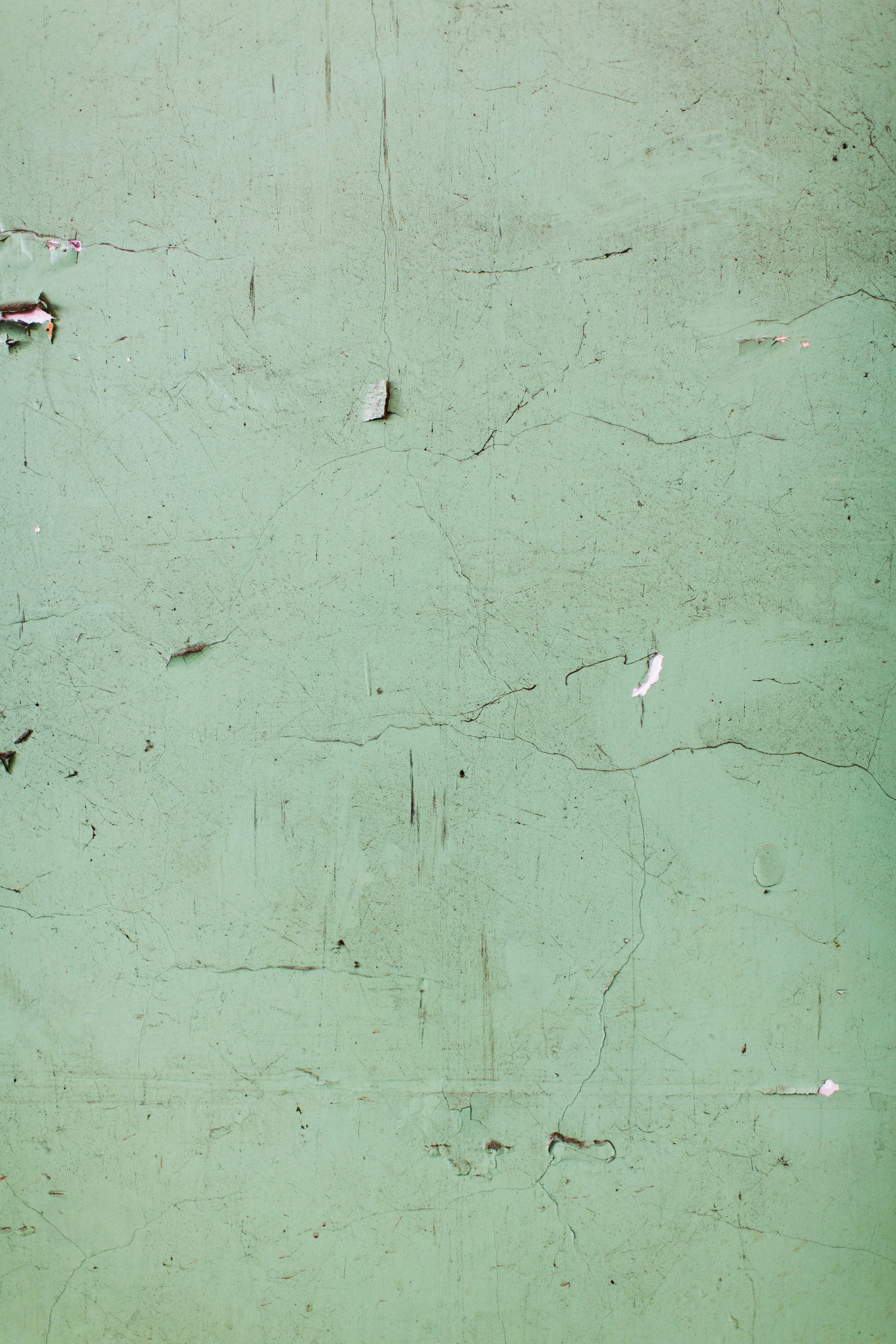 Textured green wall with visible cracks and peeling paint, revealing layers of history and wear.
