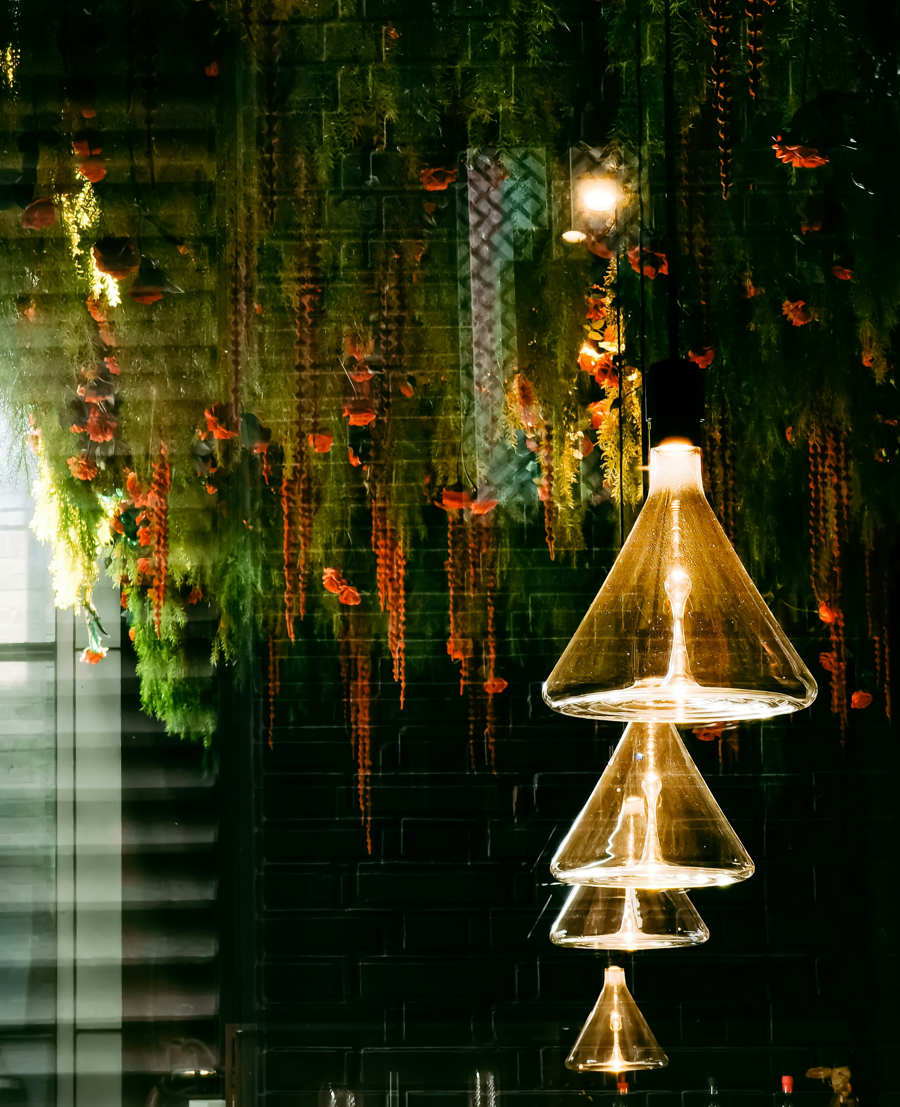 Elegant glass pendant lights hang beneath a lush canopy of greenery and vibrant flowers, creating a serene atmosphere in a modern setting.