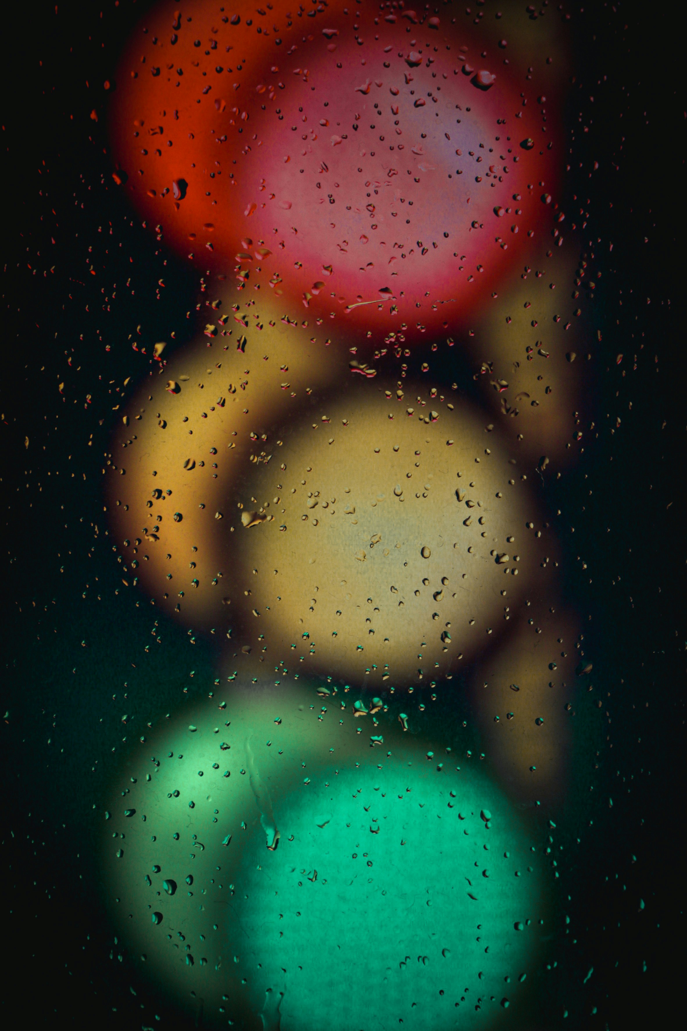 Colorful traffic lights blurred by raindrops on glass create a mesmerizing abstract effect.