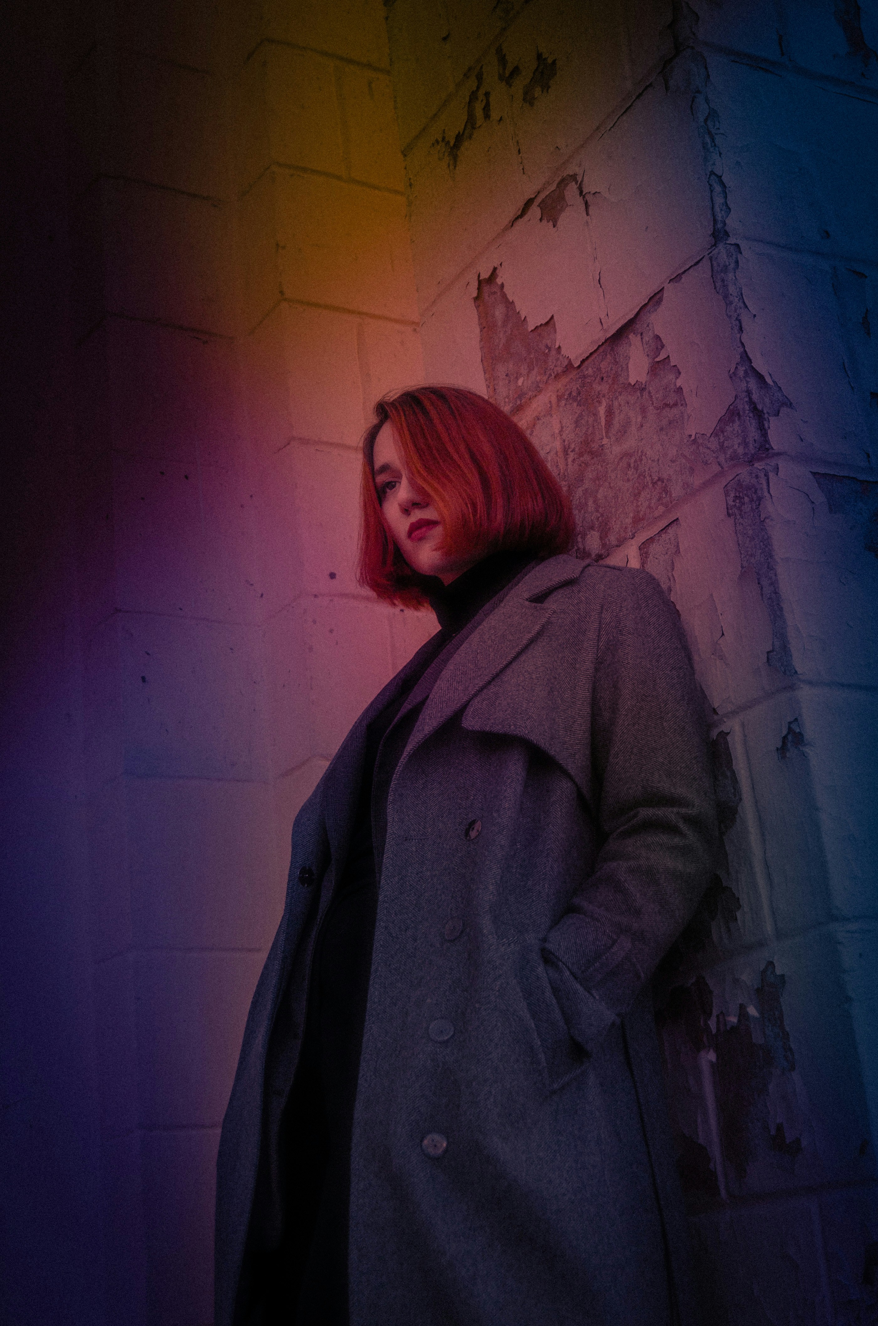 Neon-Tinted Portrait: Red-Haired Figure Against a Rainbow Brick Wall