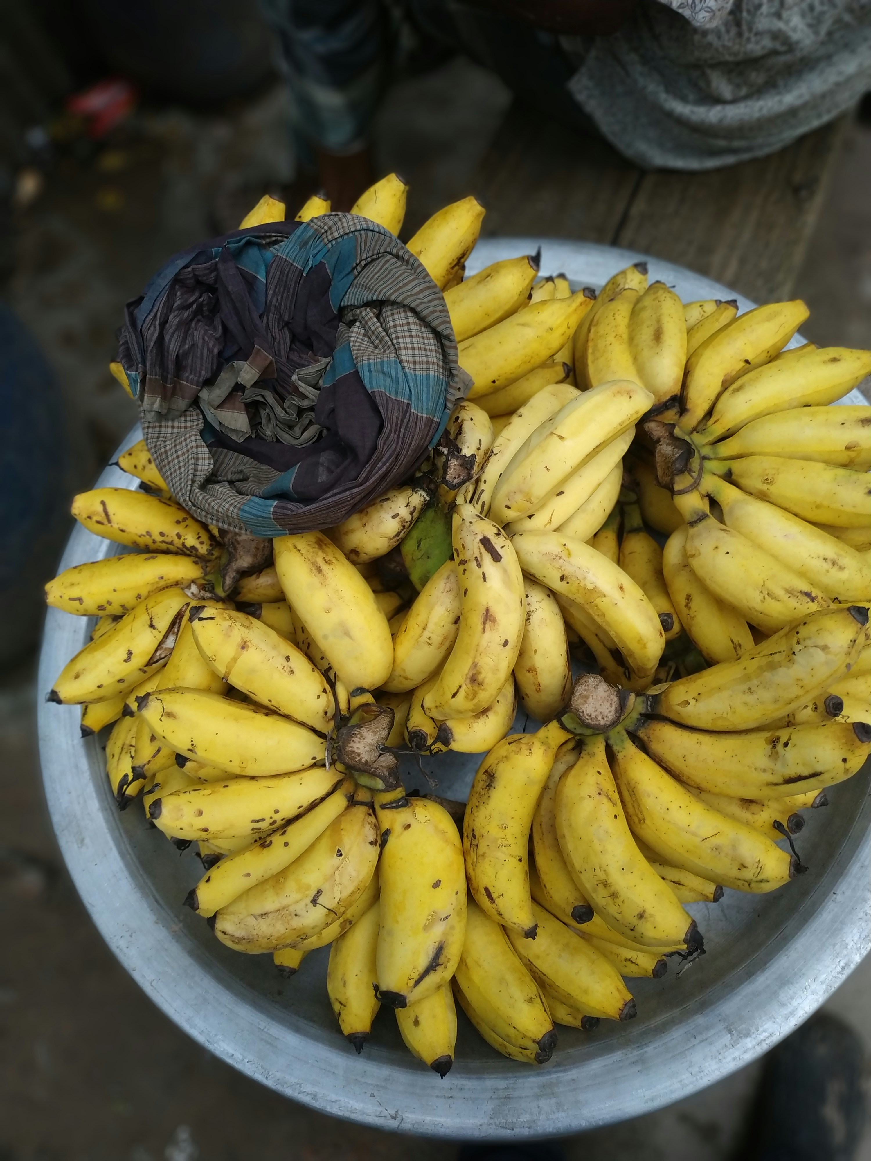 A vibrant display of ripe bananas arranged in a circular pattern, topped with a piece of cloth. The scene captures the essence of local market produce.