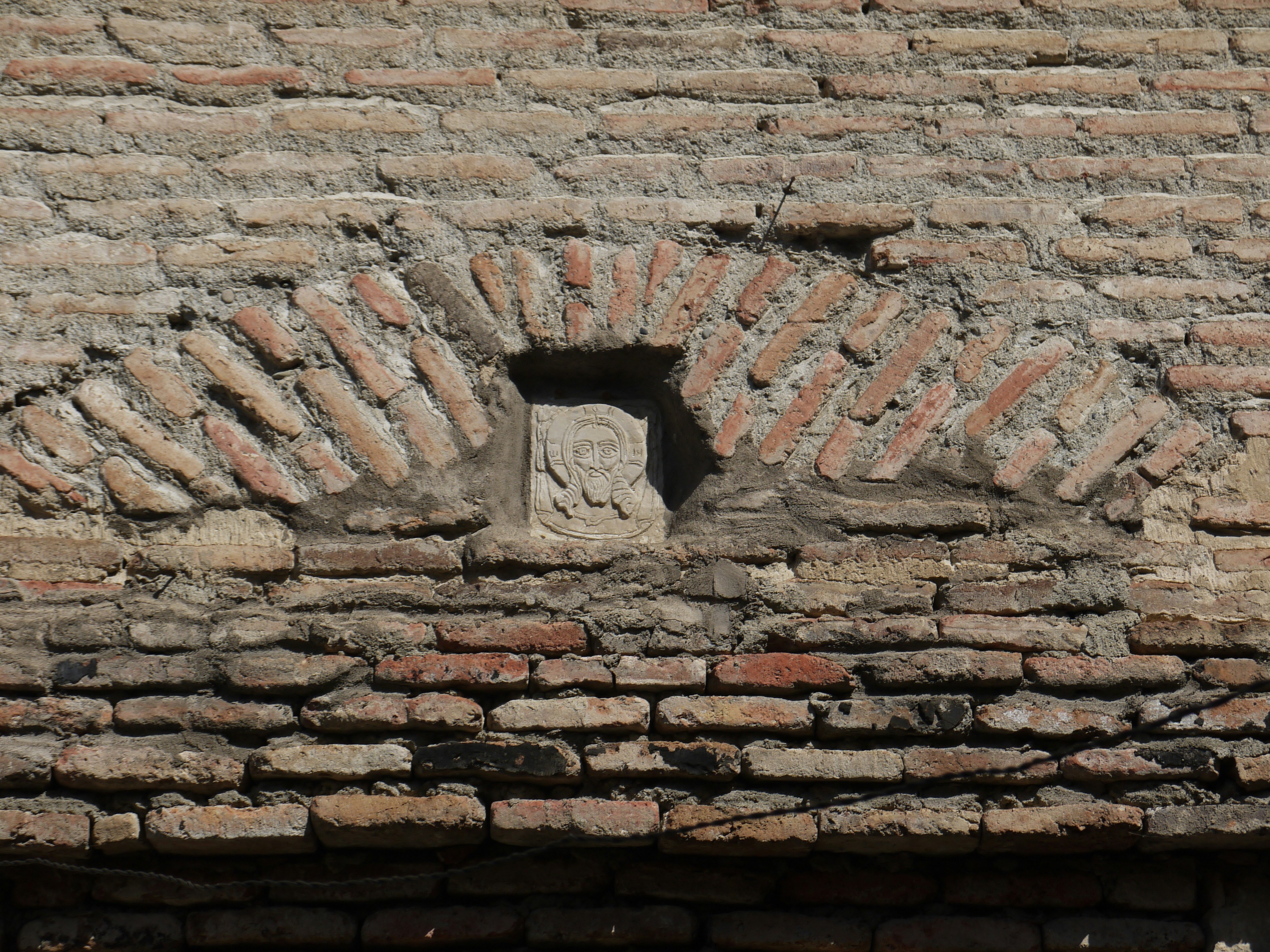 Carved stone relief of a face embedded in an arched brick wall.