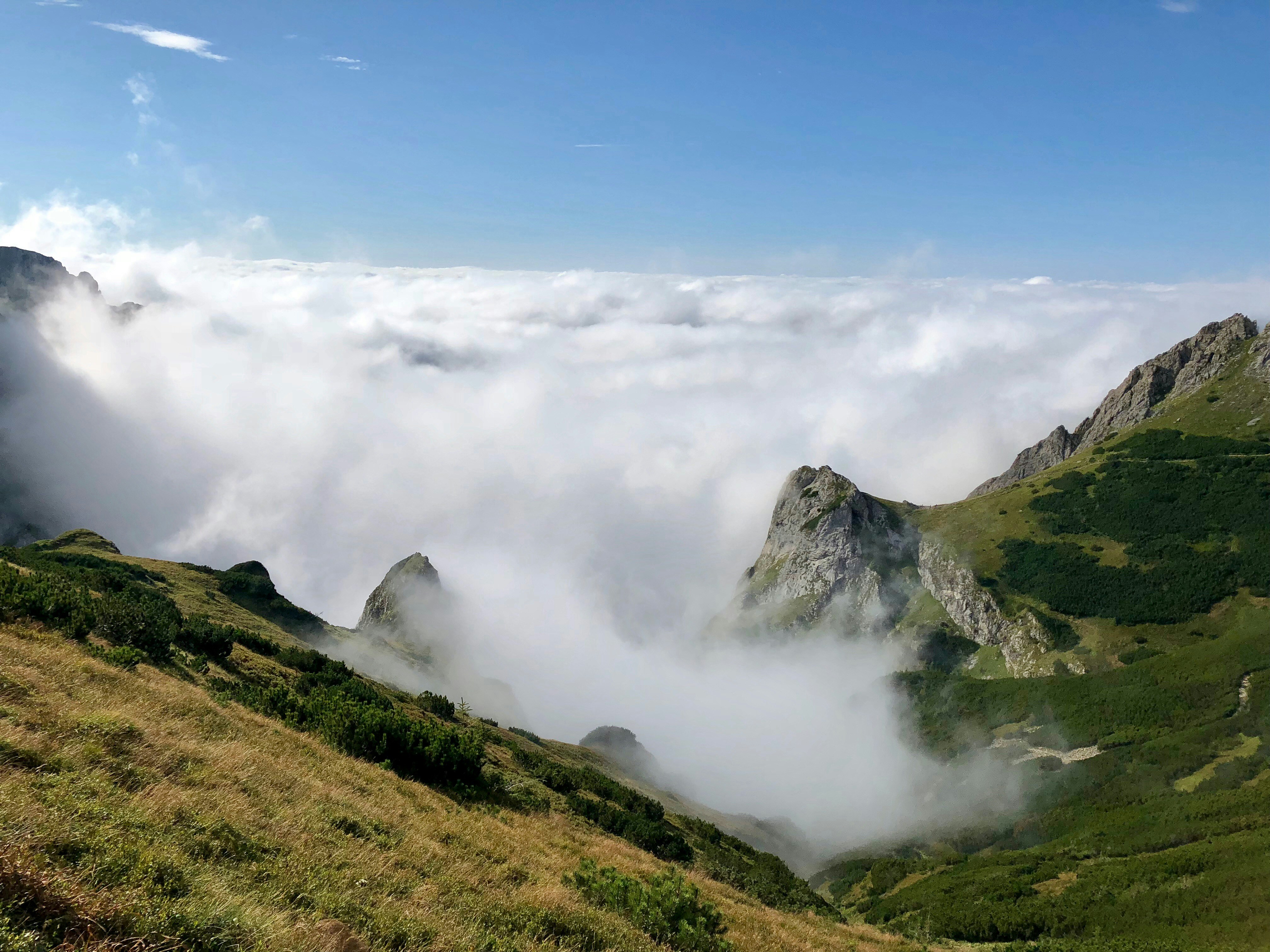 Clouds envelop mountain peaks under a clear blue sky.