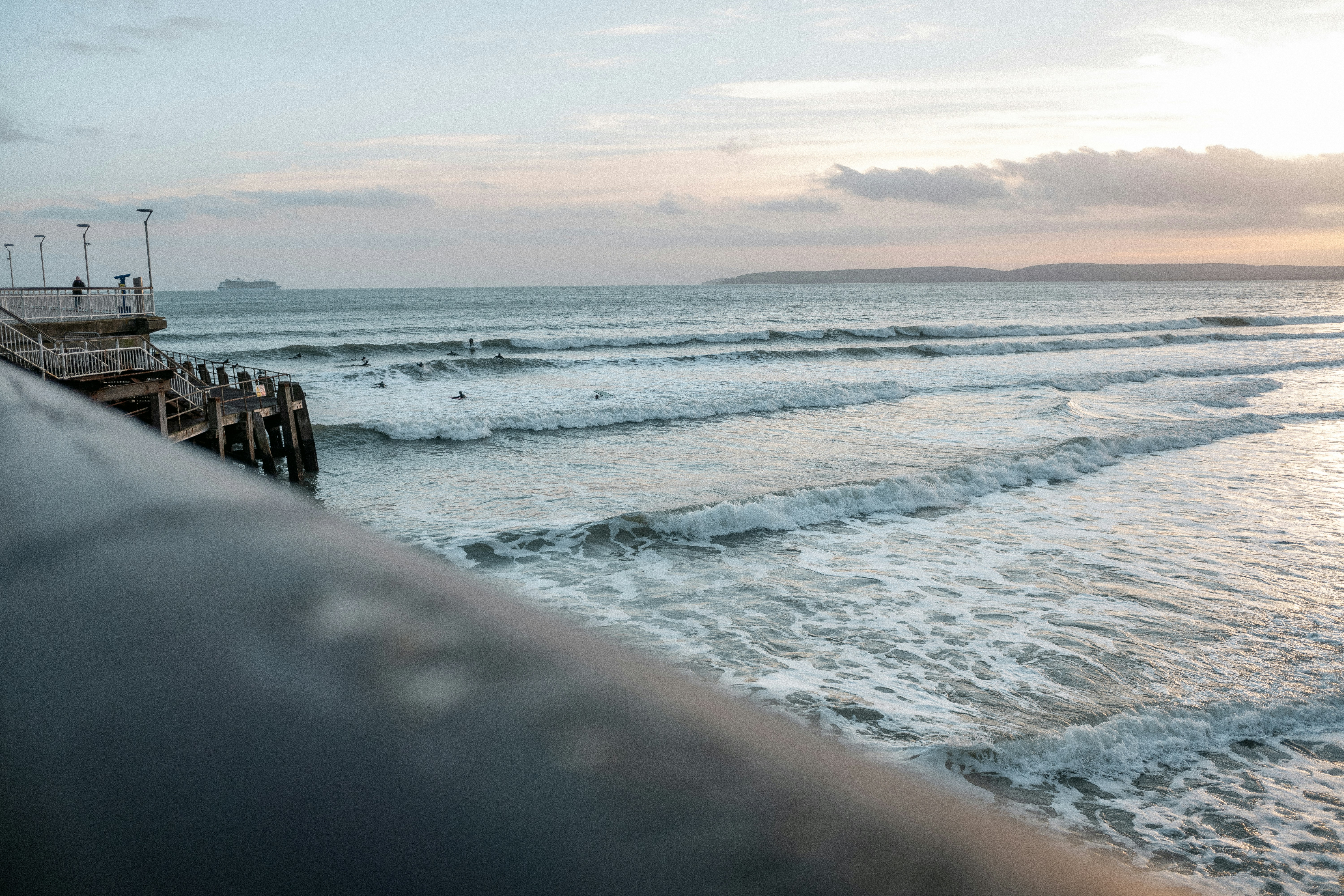 Gentle waves lap against a wooden pier under a pastel sky at sunset.