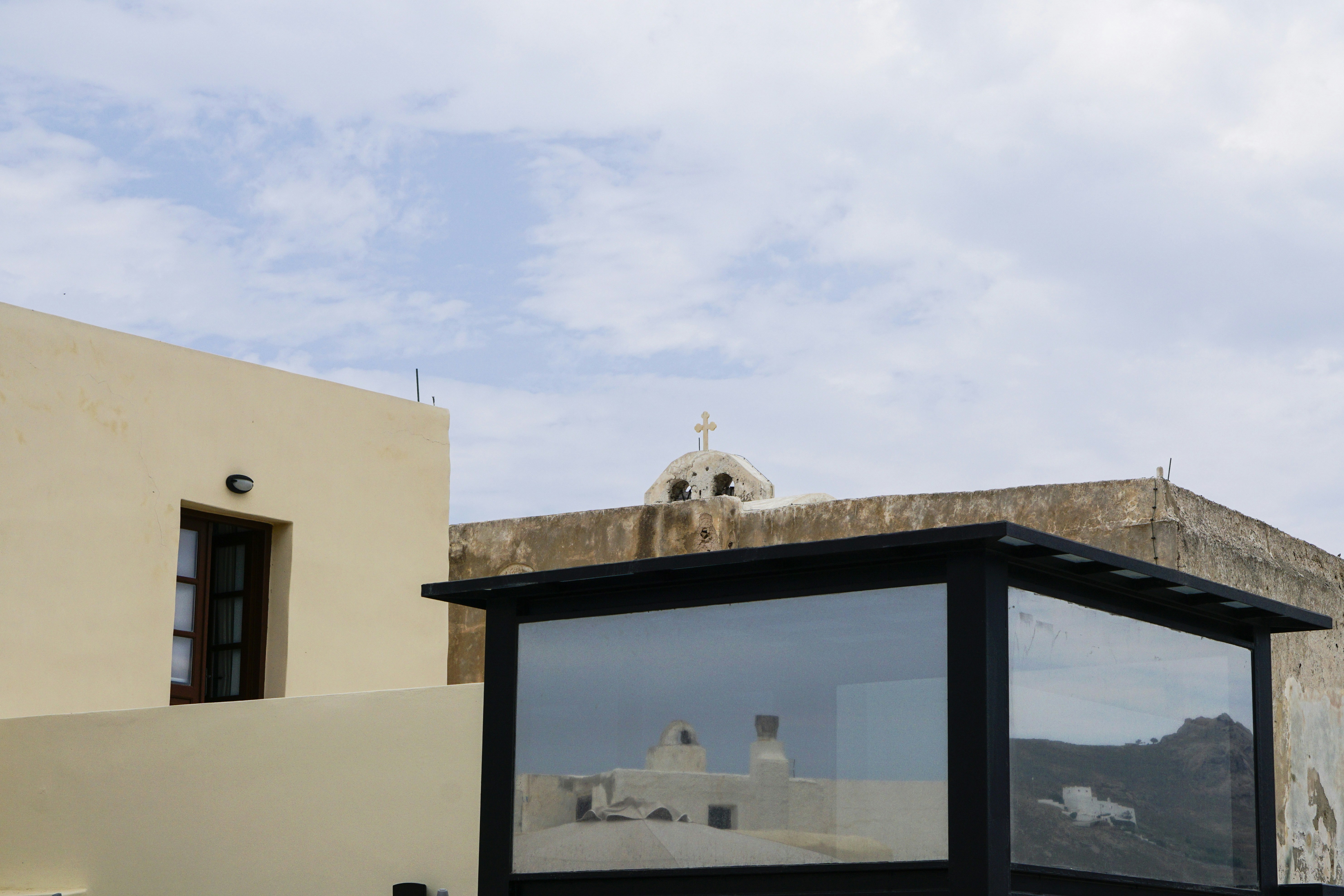 White concrete building with a cross on the rooftop under a partly cloudy sky.