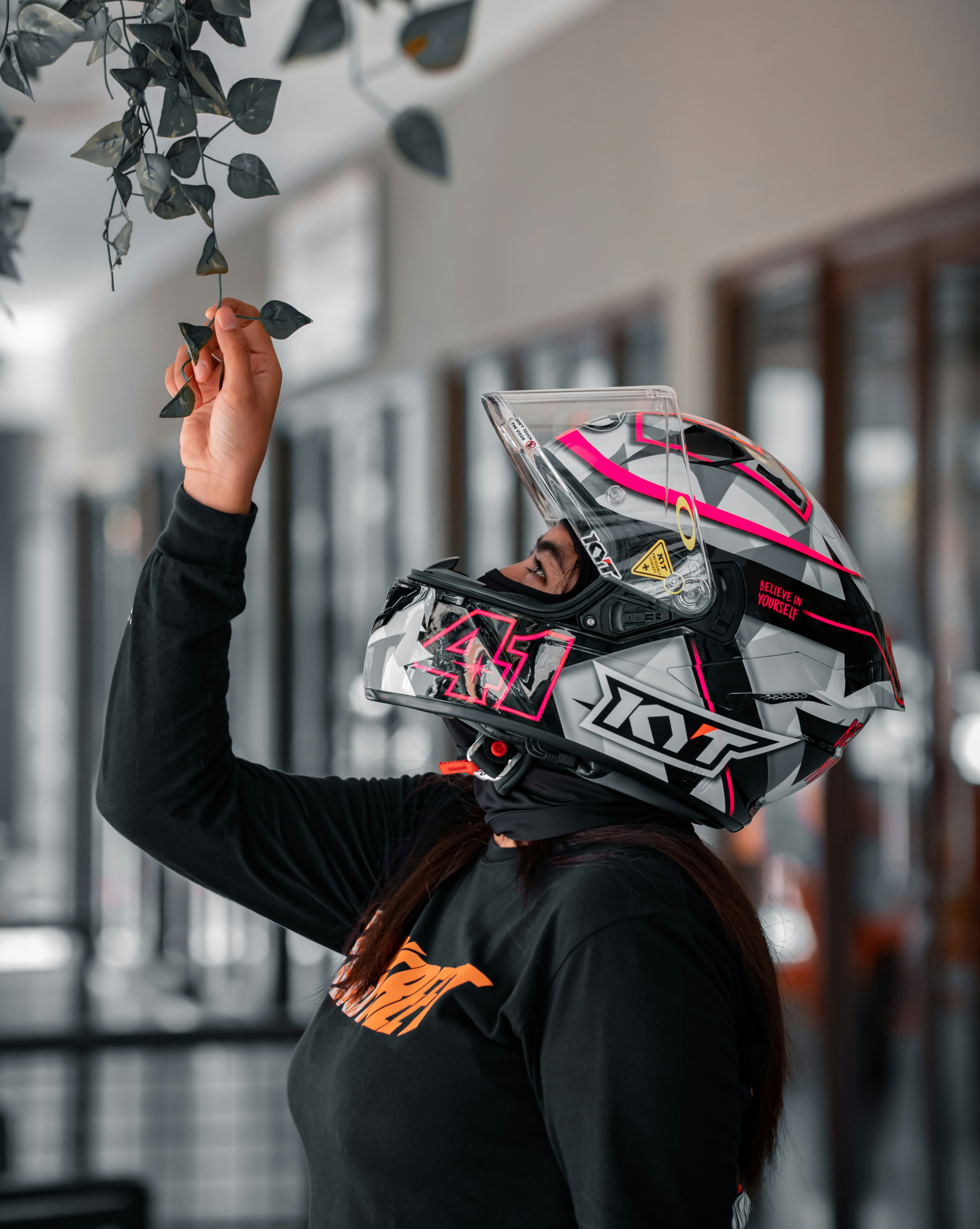 Neon-Accent Motocross Helmet Reaches Toward Indoor Foliage