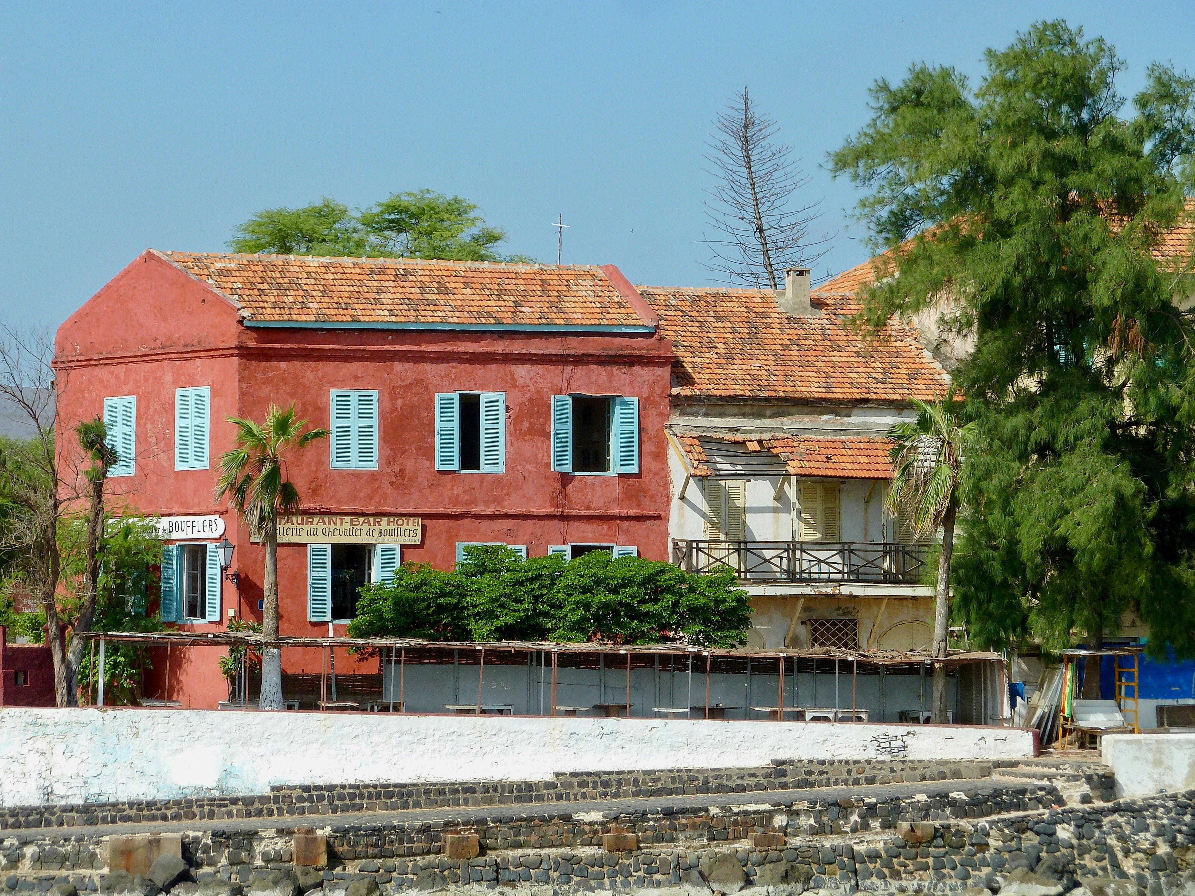 Red and beige buildings with tiled roofs surrounded by lush green trees under a clear sky.