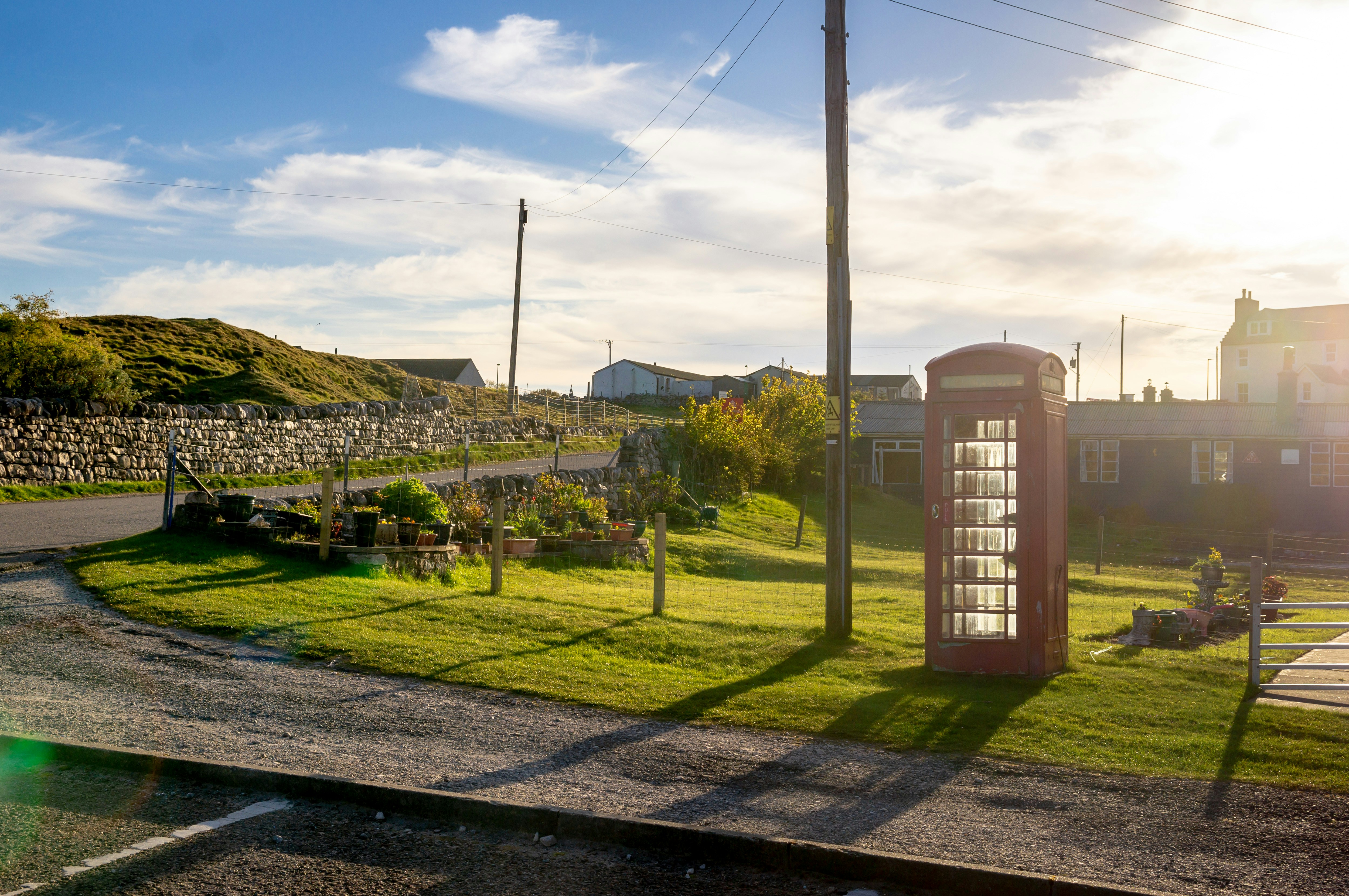 Red Phone Booth in Golden Hour: A Quiet Village Lawn Framed by Stone Wall