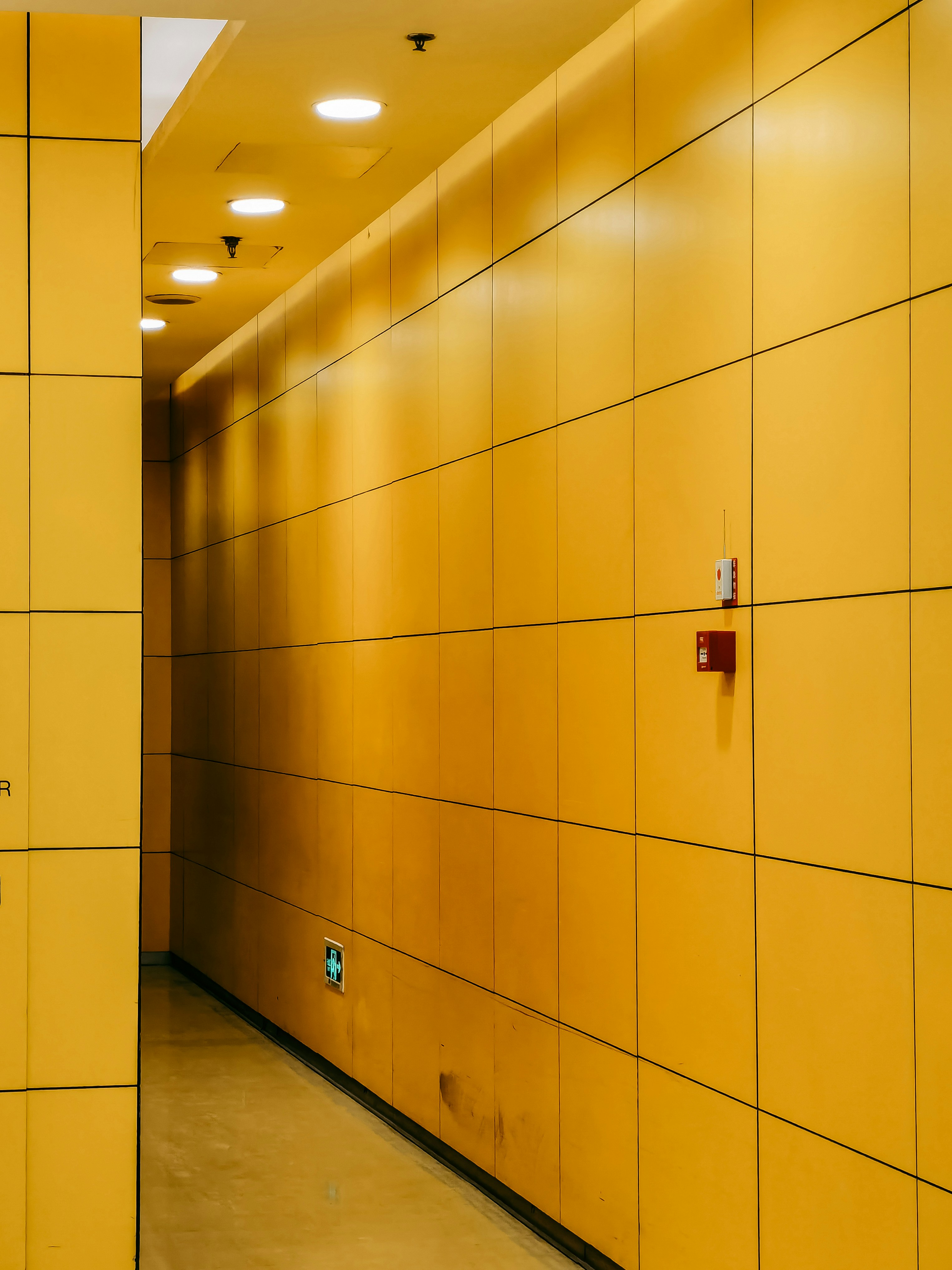 An interior corridor of warm amber panels stretches toward a dim vanishing point, illuminated by ceiling lights. The shot emphasizes architectural geometry and the soft glow that defines the space.