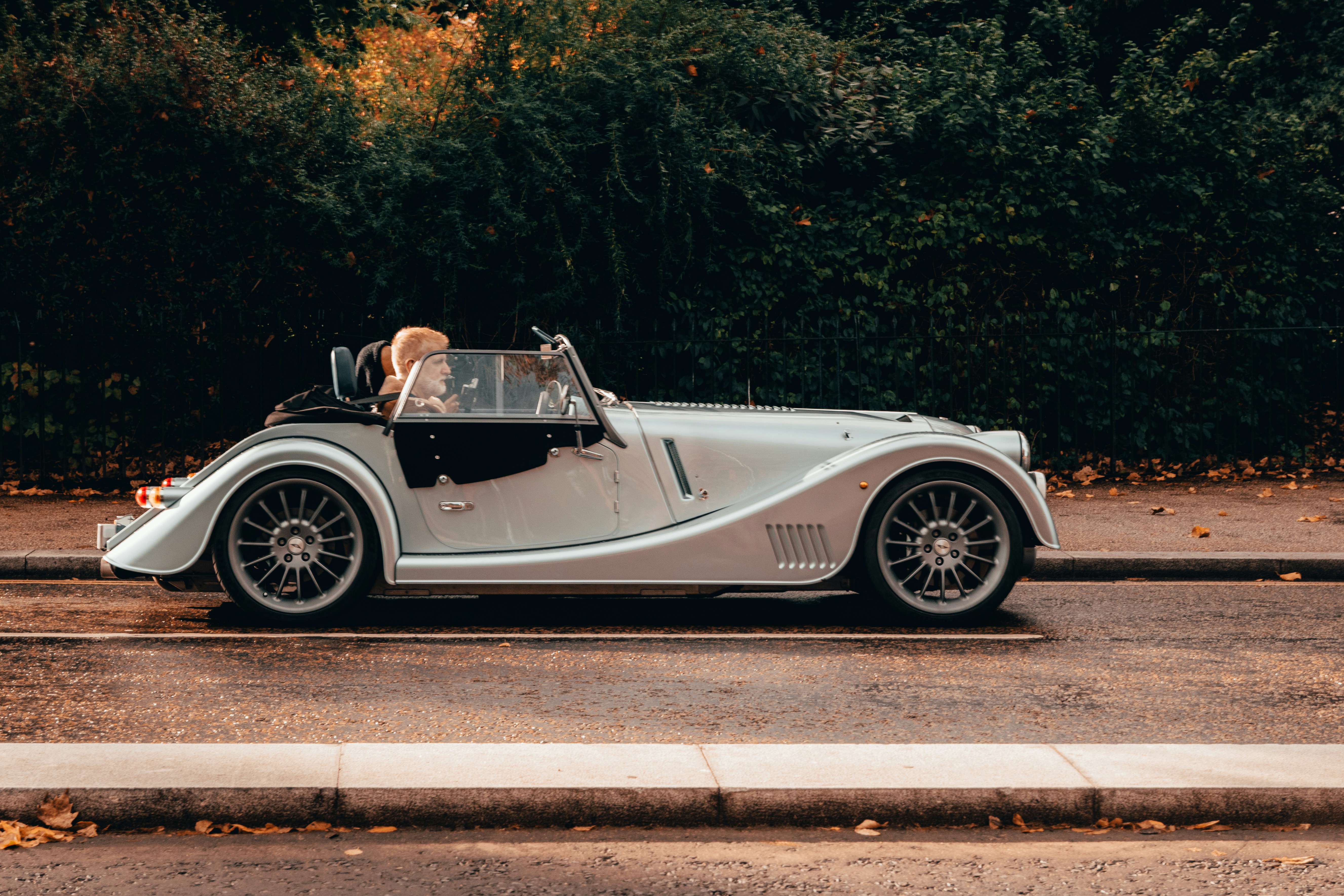 Vintage convertible sports car parked on a tree-lined street during the day.