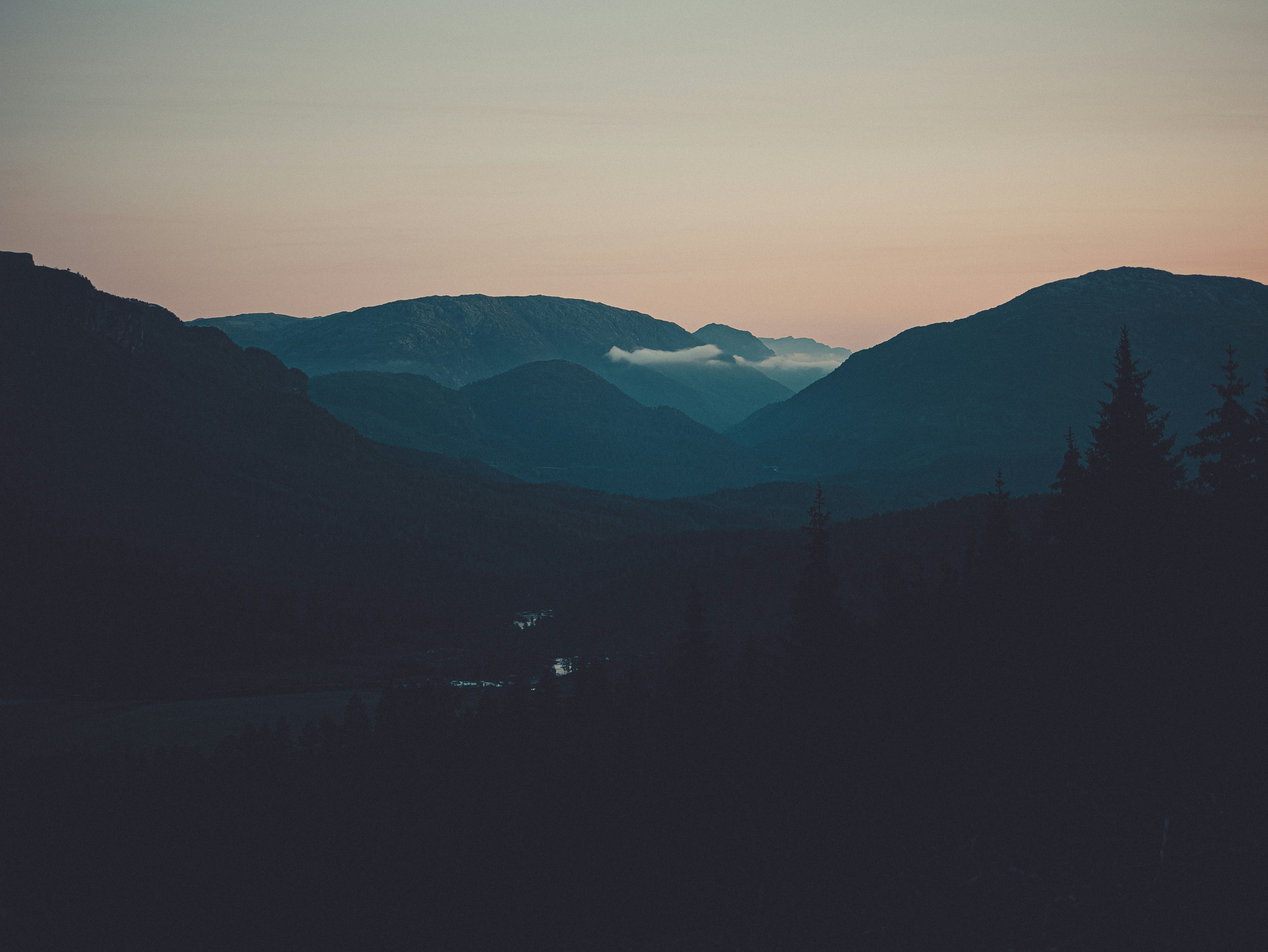 Silhouetted mountains under a soft twilight sky, with mist gently rolling through the valleys. The tranquil scene evokes a sense of peace and solitude.