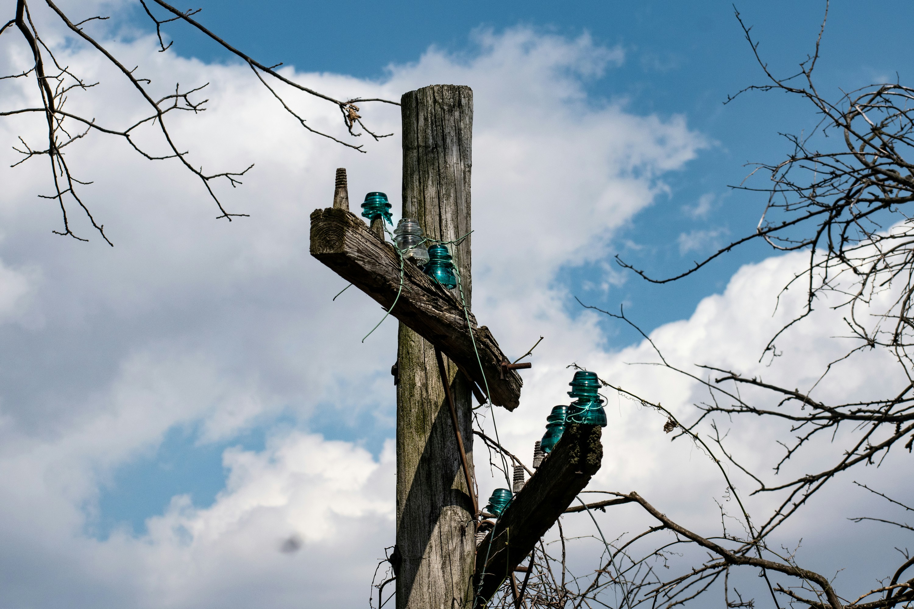 Weathered Crossarm with Teal Glass Insulators Against a Bright Sky