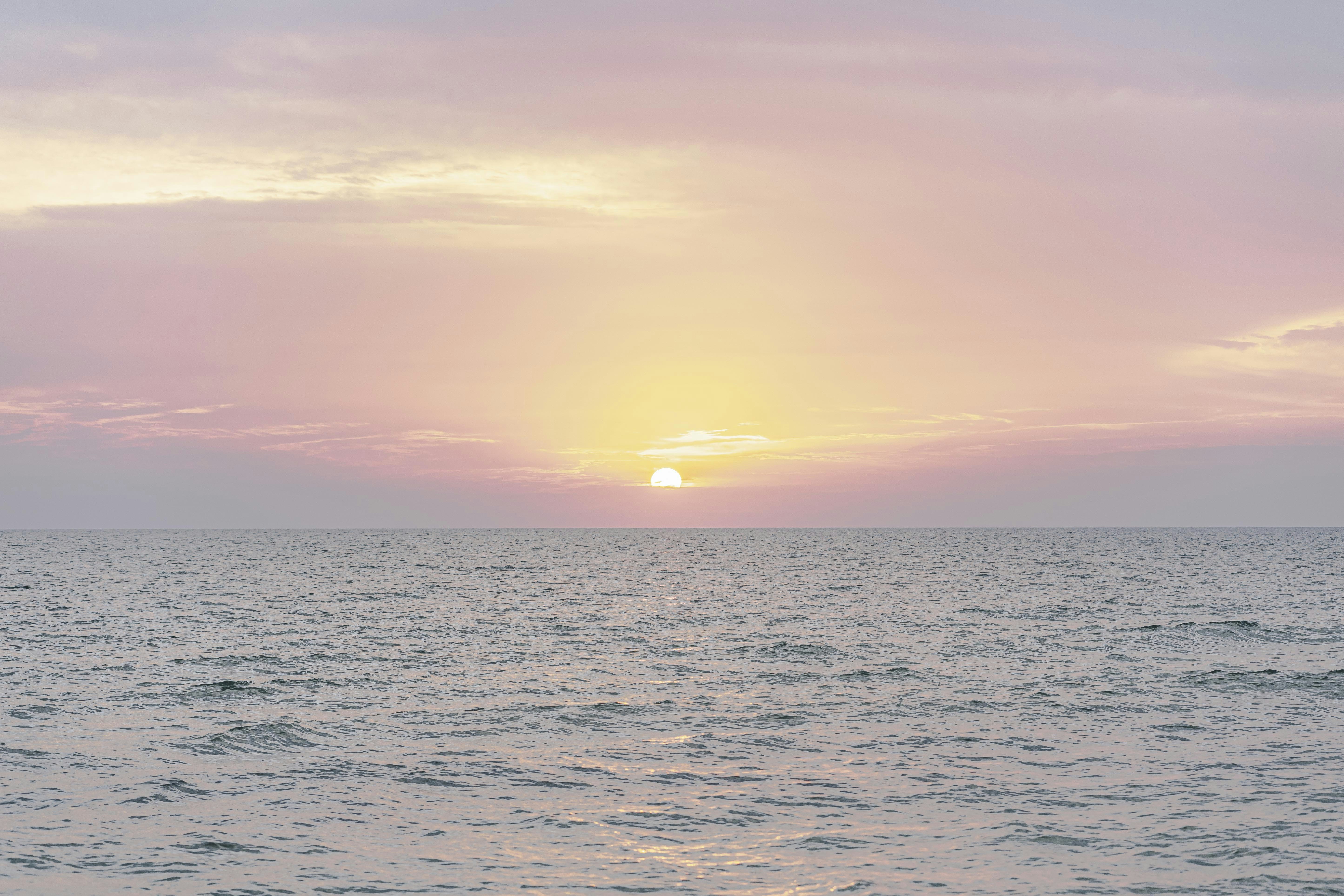 Sunrise casting soft pink and orange hues over a calm ocean horizon.
