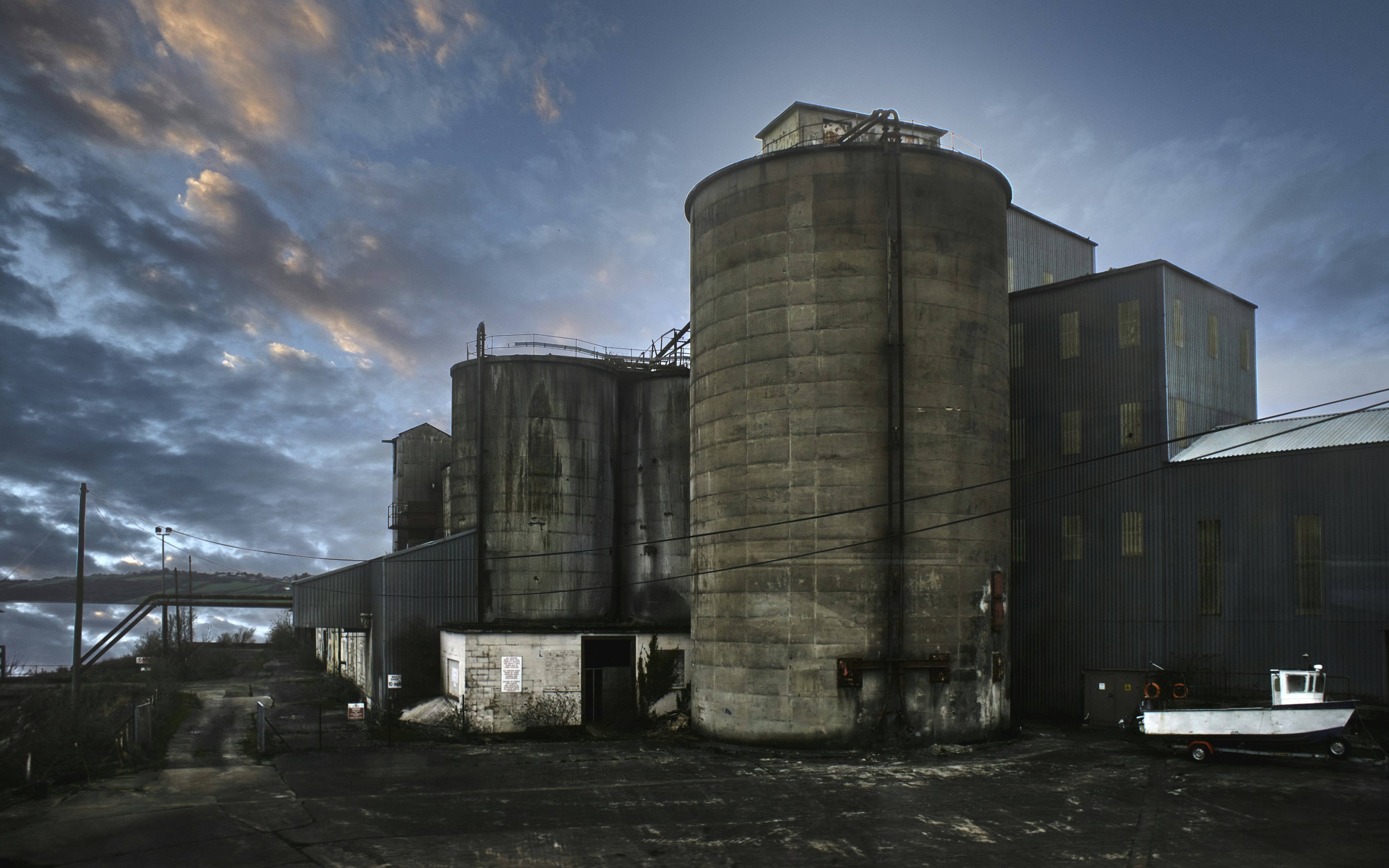 An old warehouse/factory with a fishing boat in the parking lot at Magheramorne train station in County Antrim (Jan., 2020)