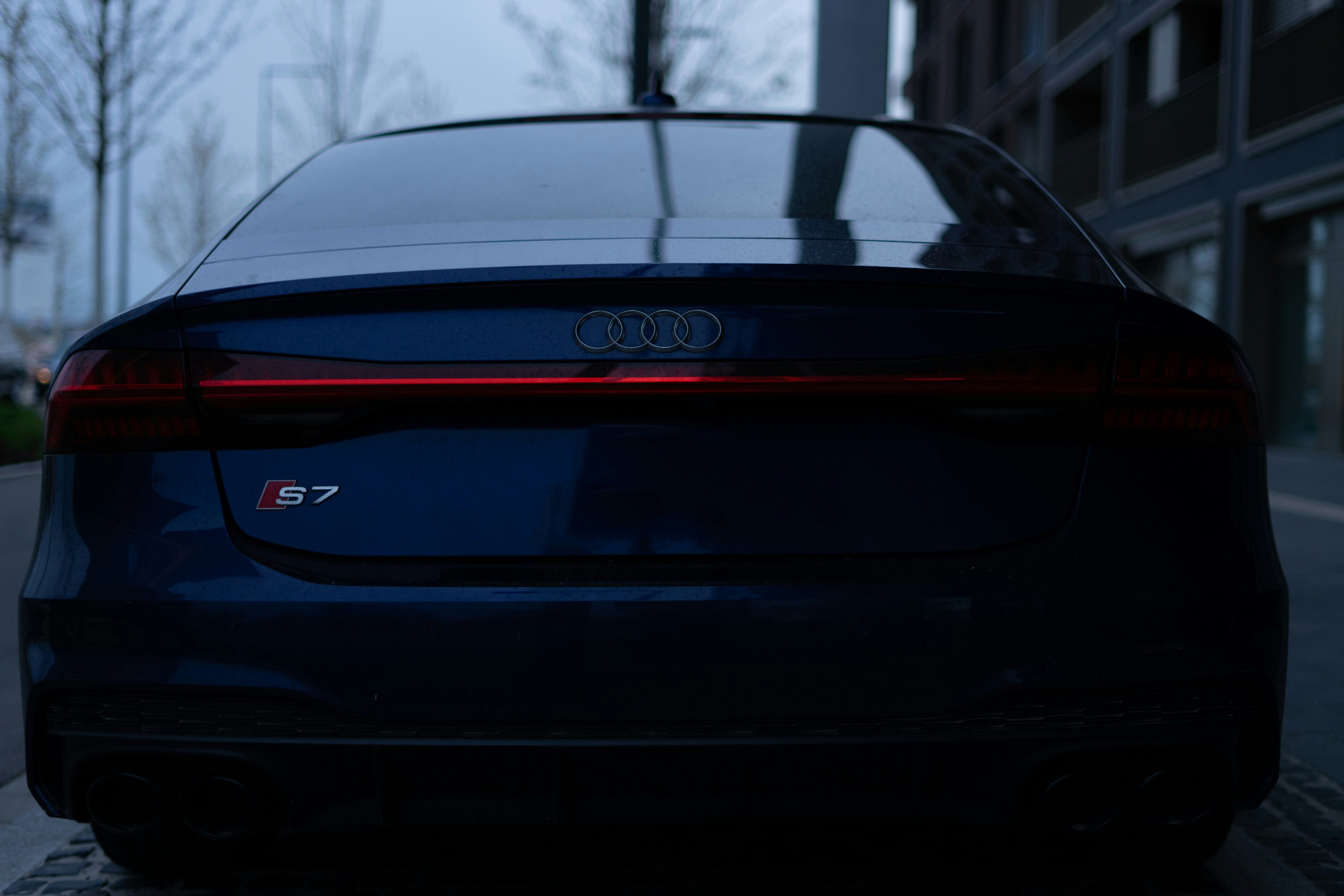 Rear view of an Audi S7 parked in an urban setting, showcasing its sleek design and distinctive taillights.