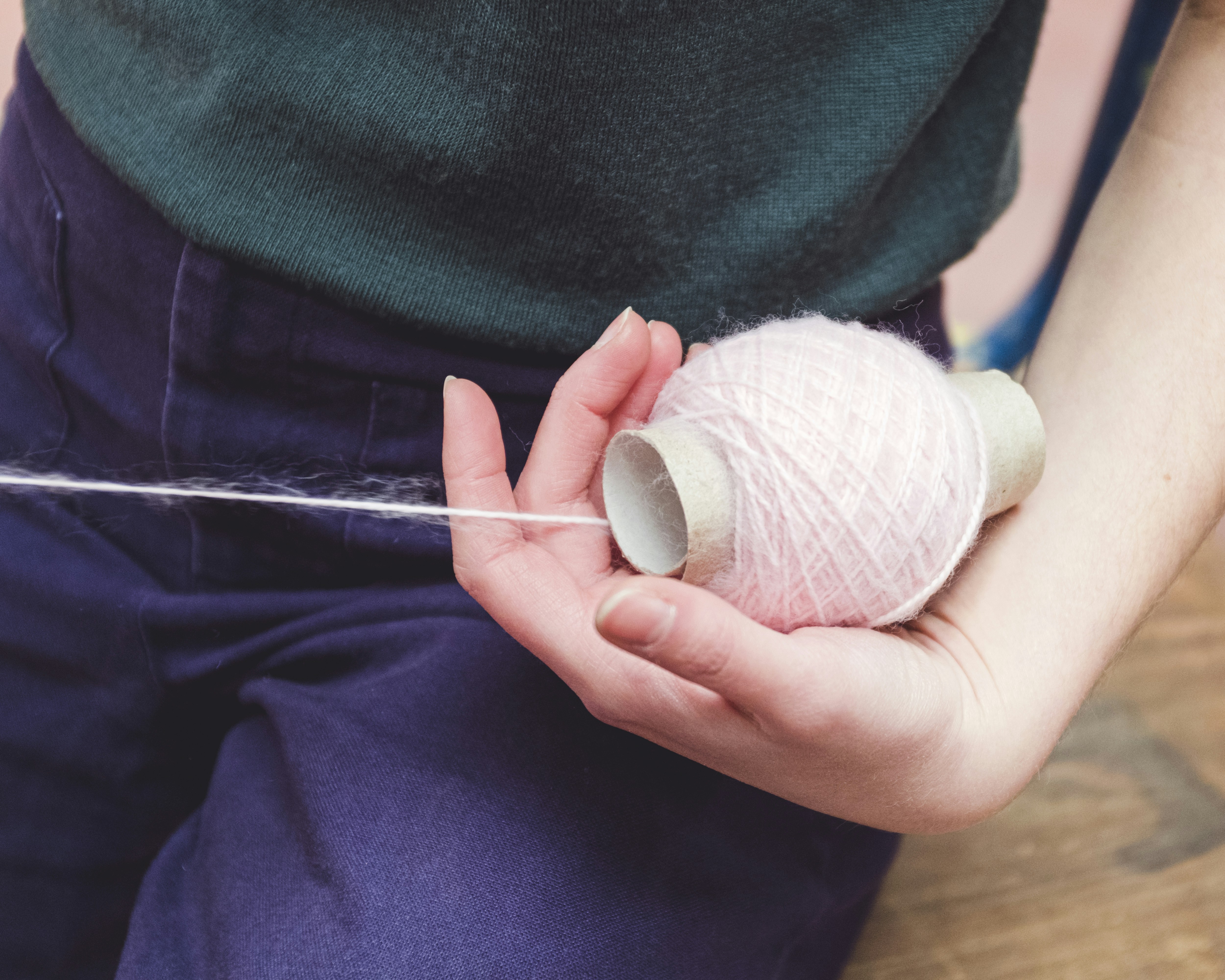 Soft pink thread wound on a spool held delicately between fingers, set against a warm, textured background.