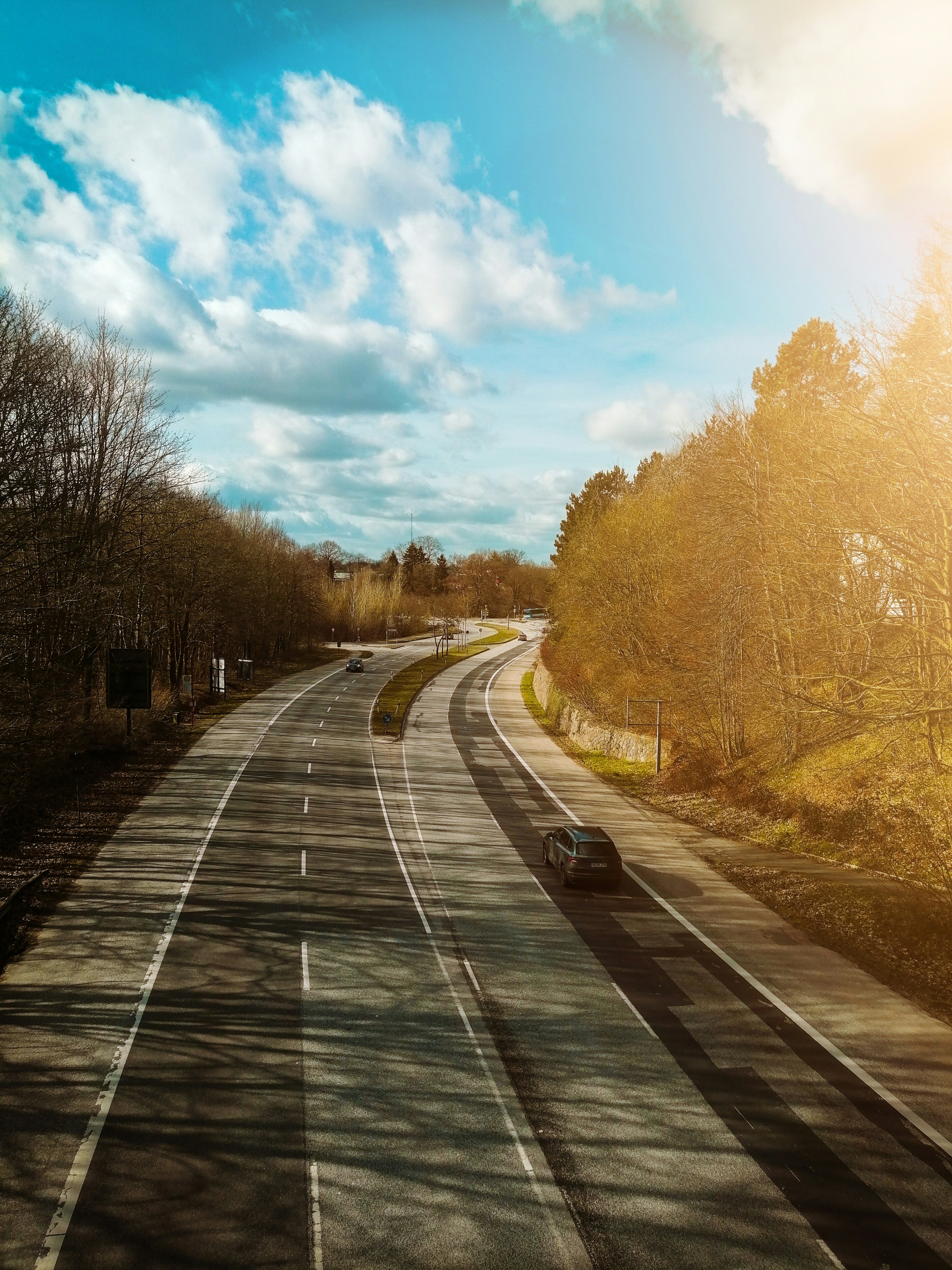 A winding road curves through a landscape adorned with autumn foliage under a bright blue sky with fluffy clouds.
