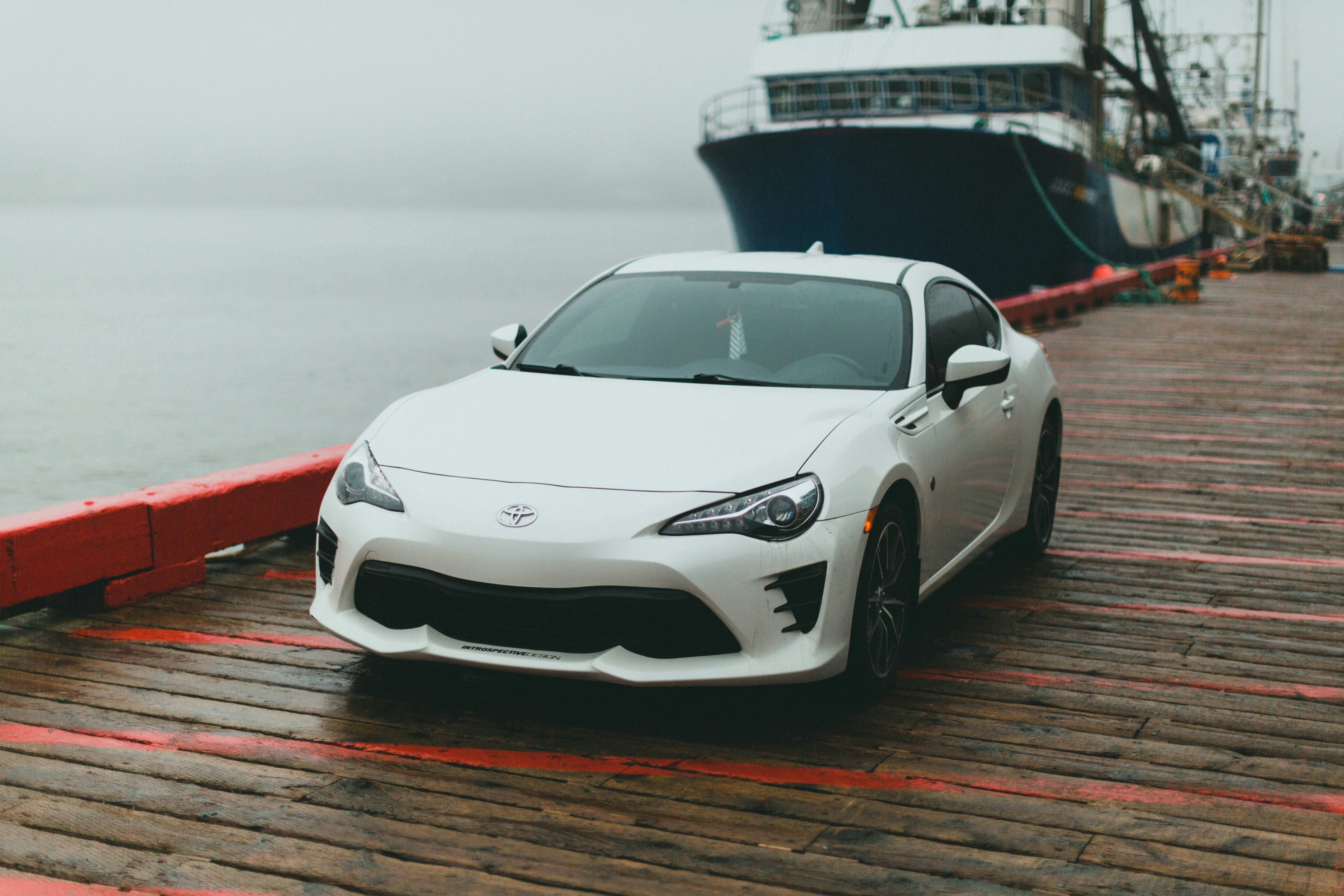 White sports sedan at a weathered dock with a large freighter looming in the background