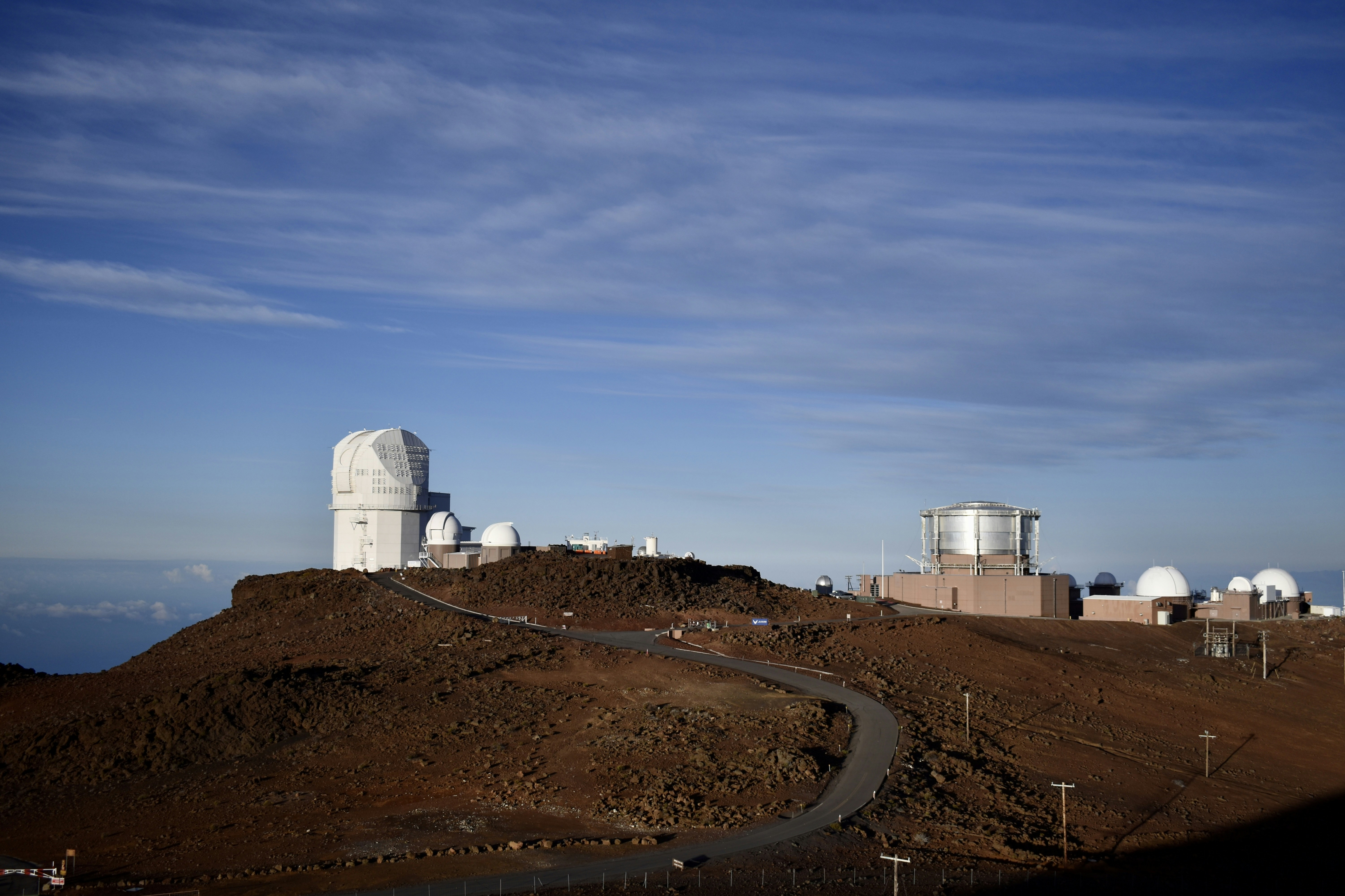 Remote observatory complex perched on a barren hill under a wide blue sky.