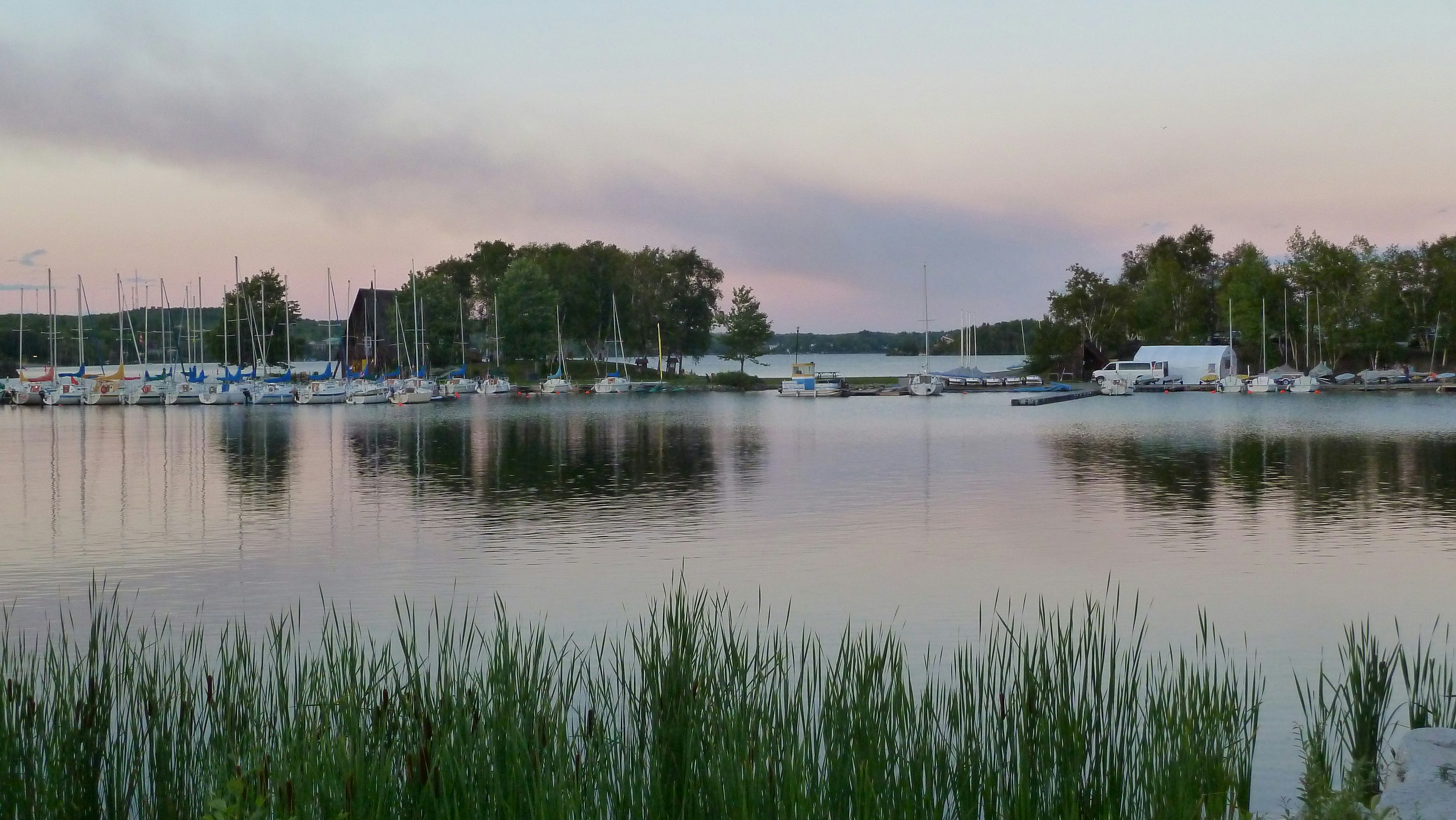 Serene lake at twilight with boats moored and trees silhouetted against a pastel sky.