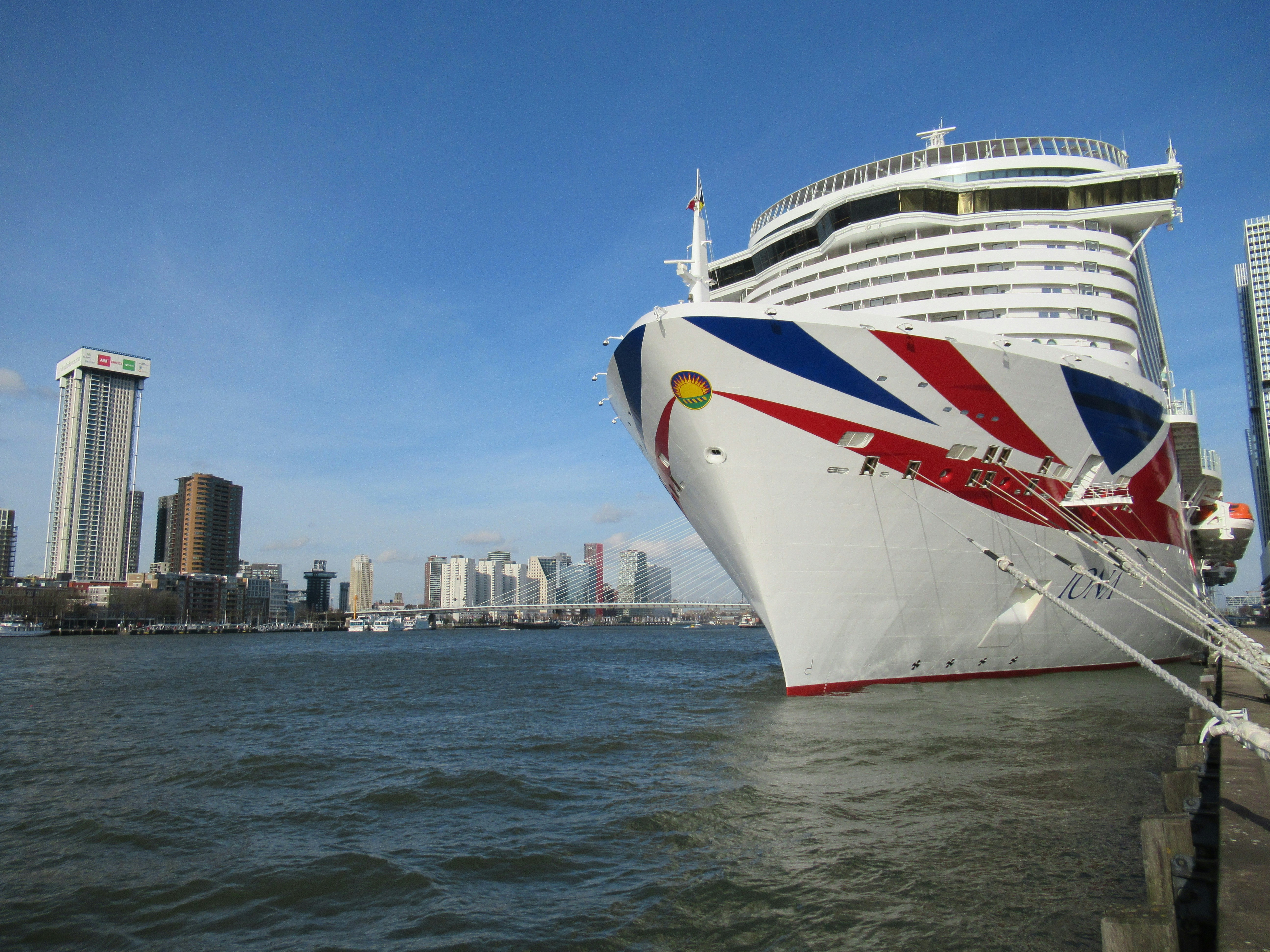 Large cruise ship with bold red and blue patterns docked near a cityscape under a clear blue sky.